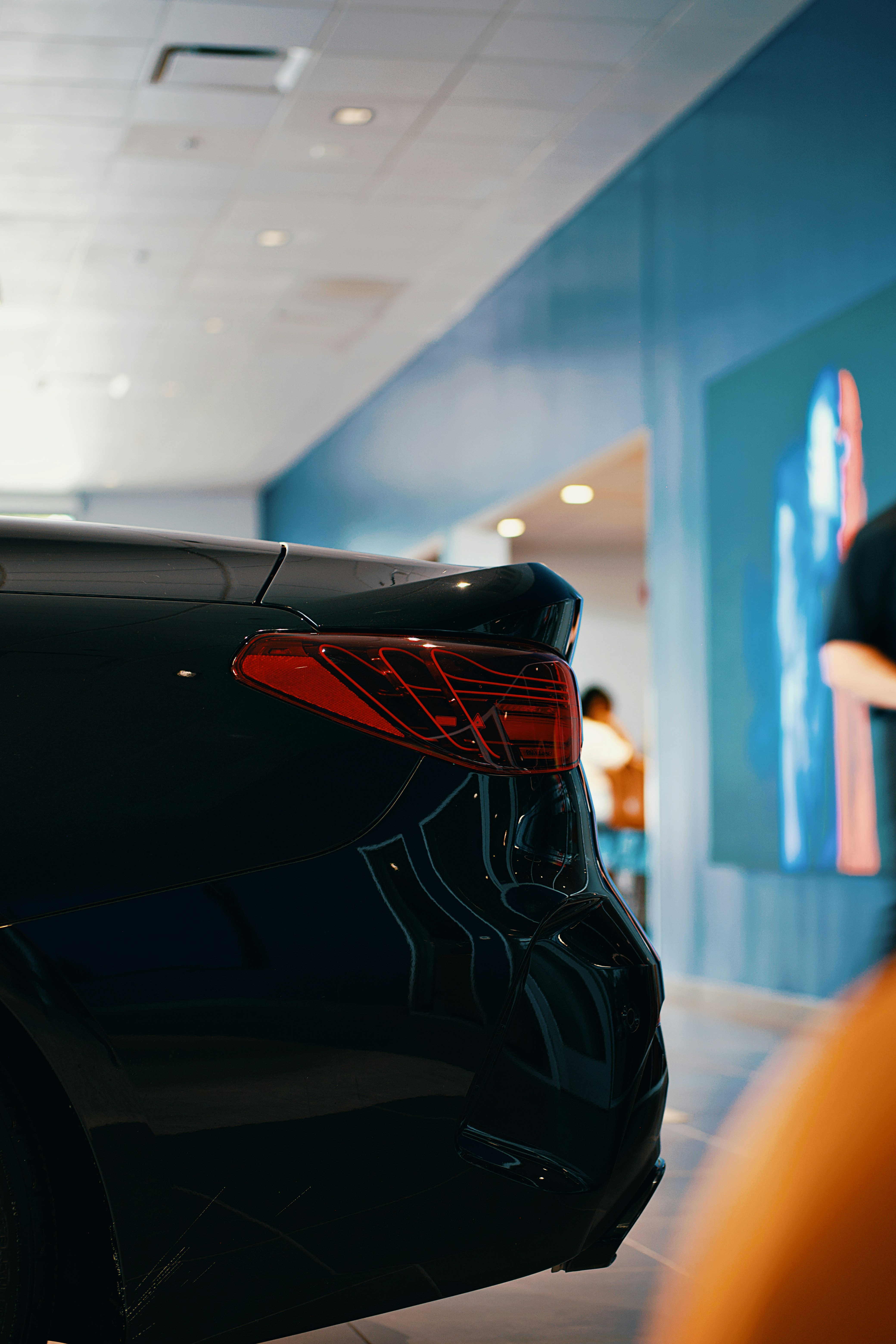 Sleek rear profile of a black luxury car in a modern interior setting, highlighting its refined design elements. A vibrant mural adds a contemporary touch to the backdrop.
