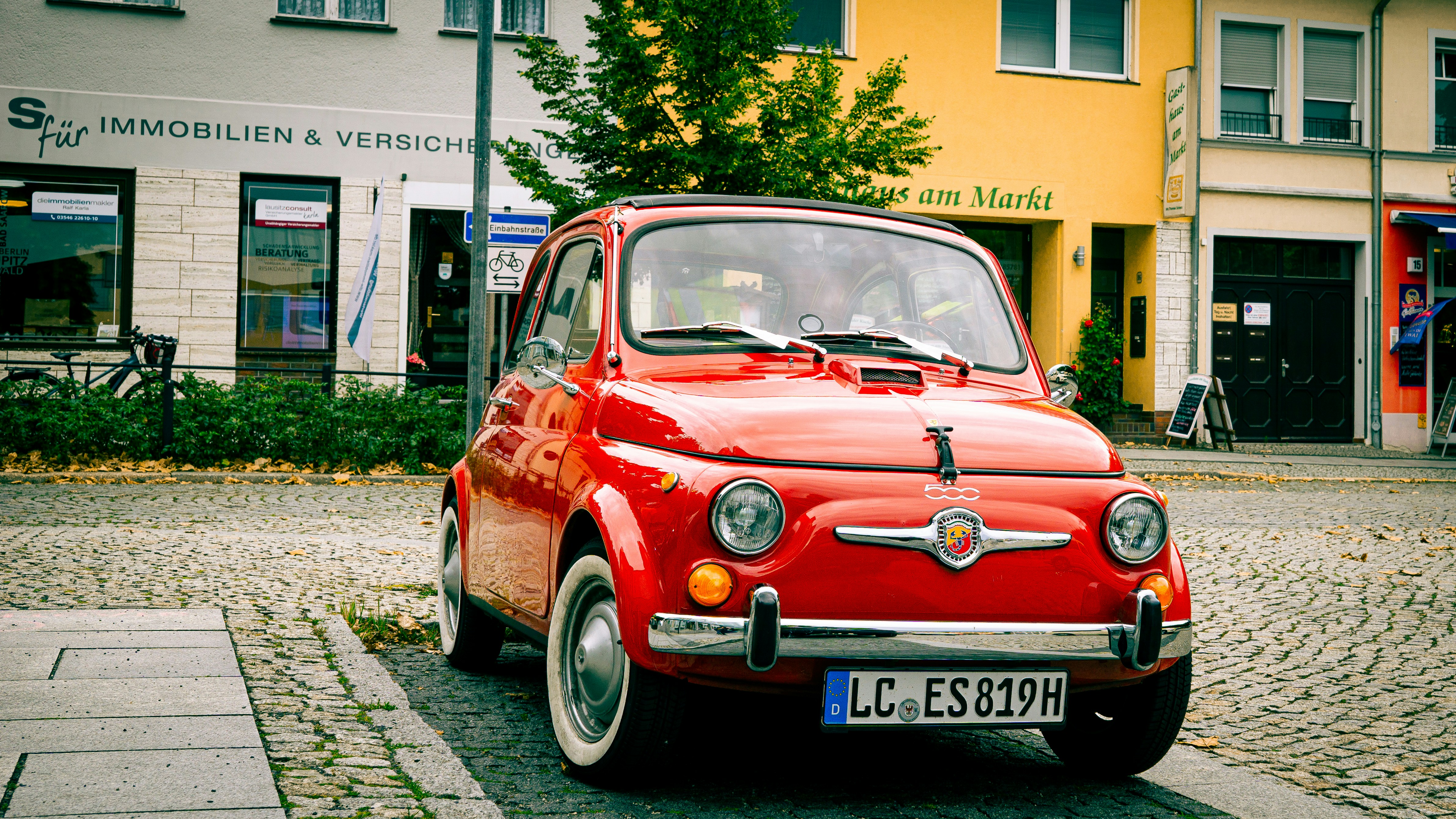 Ein Roter Abart fiat 500 in lübben | A red vintage car parks on a cobblestone street.