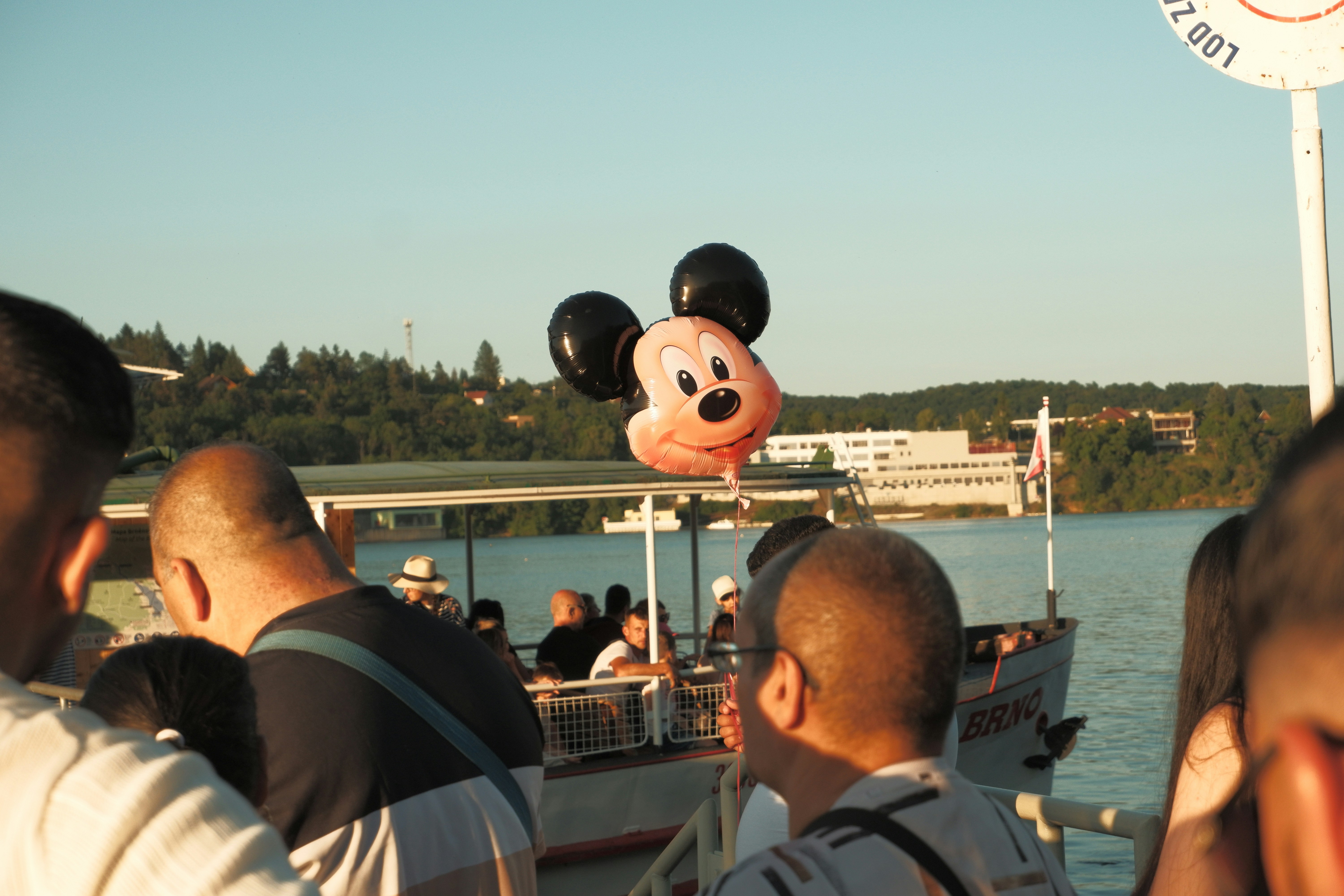 A mickey mouse balloon floats near a boat.