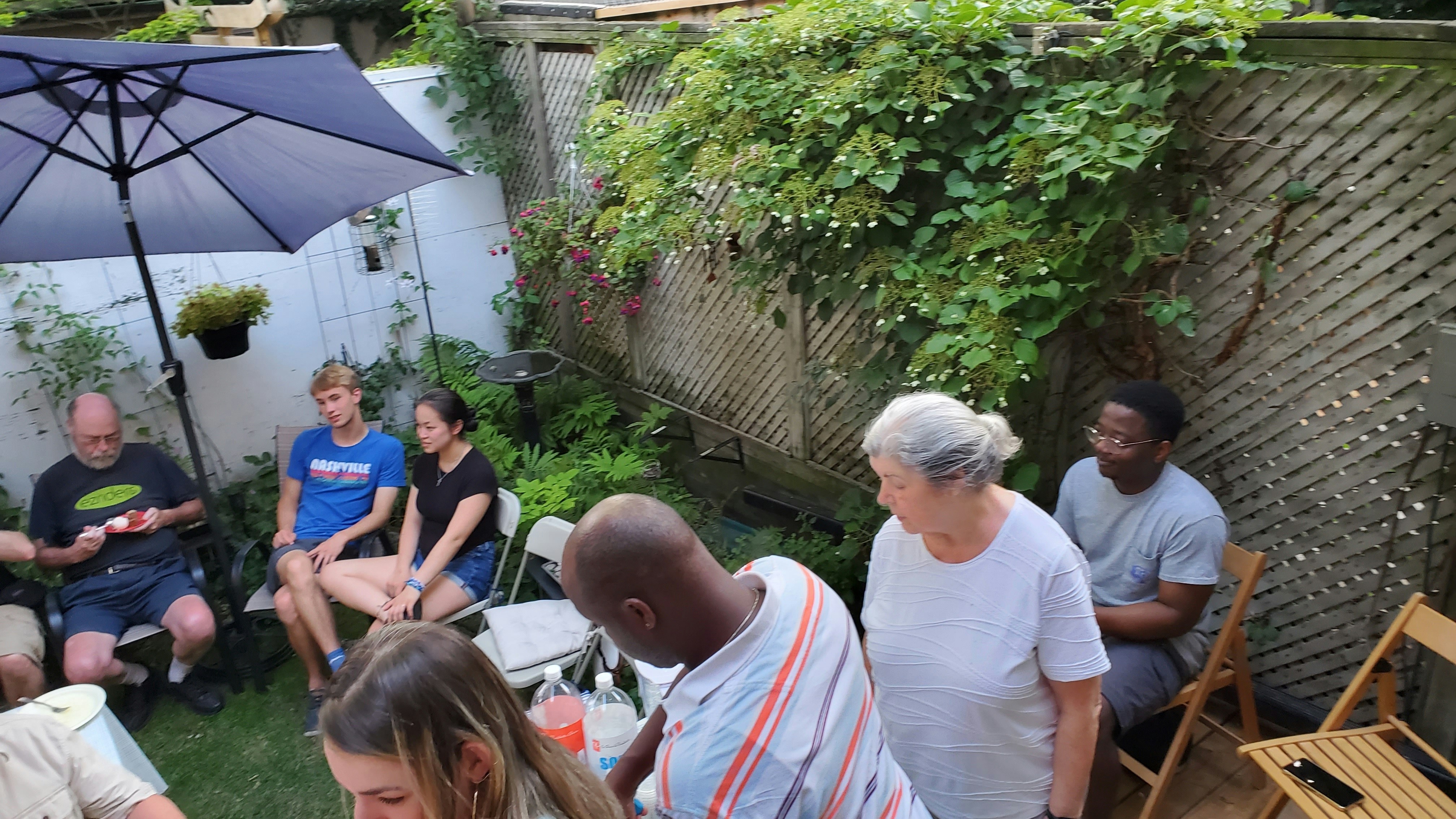 A backyard gathering with friends enjoying each other's company under an umbrella, surrounded by greenery and a cozy atmosphere.