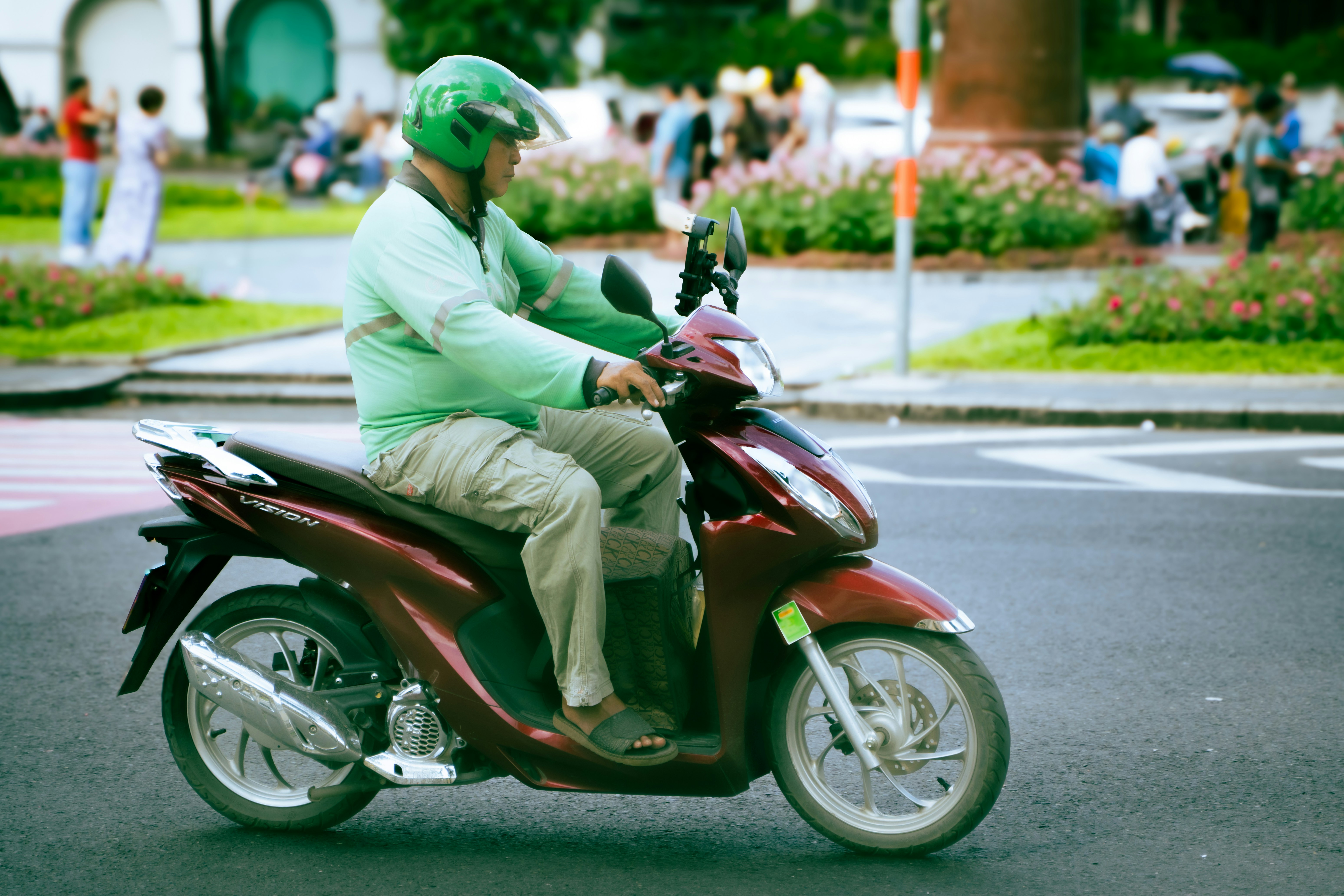 A rider in a green helmet navigates a bustling street on a maroon scooter, surrounded by a lively city backdrop.