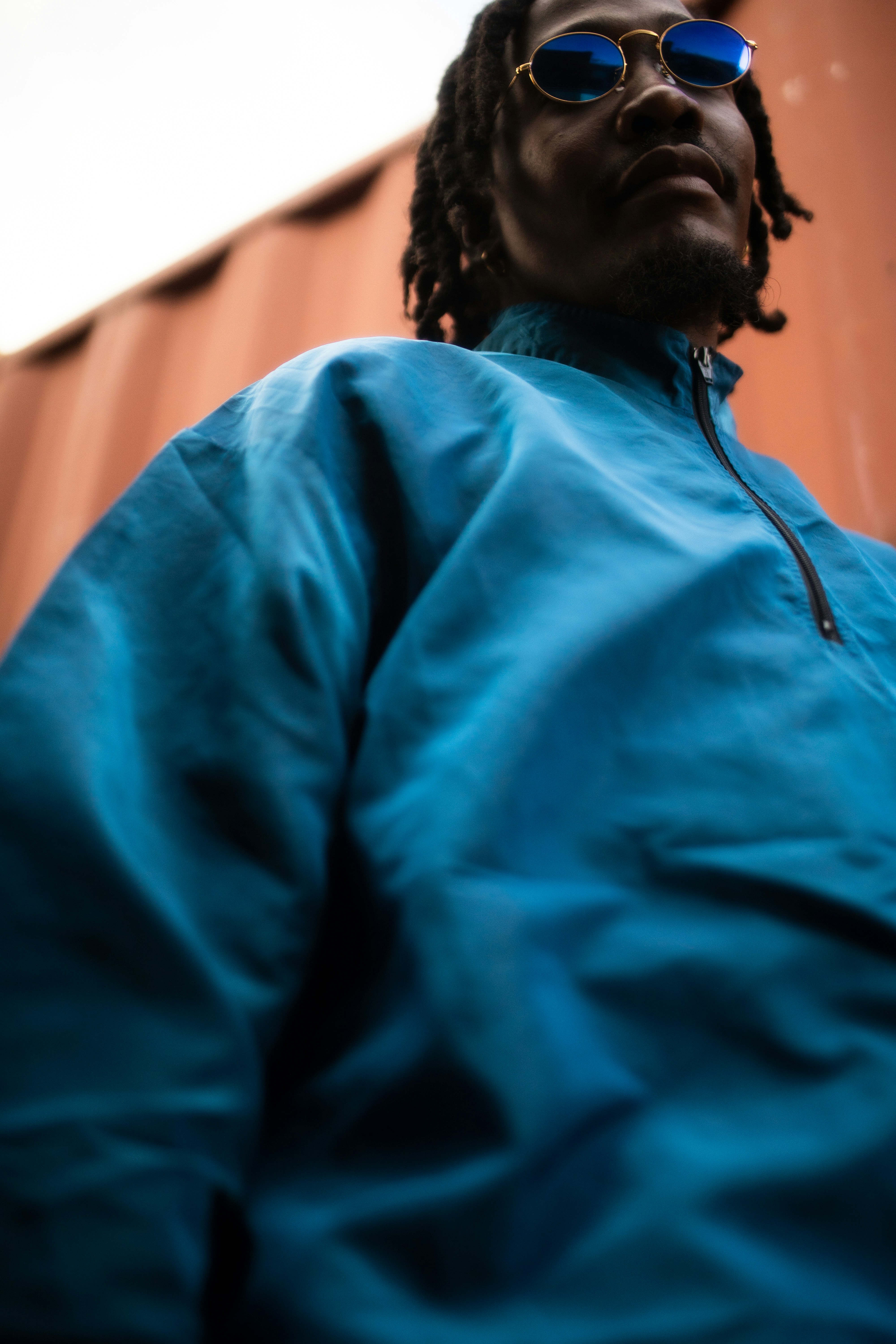 Man poses confidently, wearing sunglasses and a blue jacket.