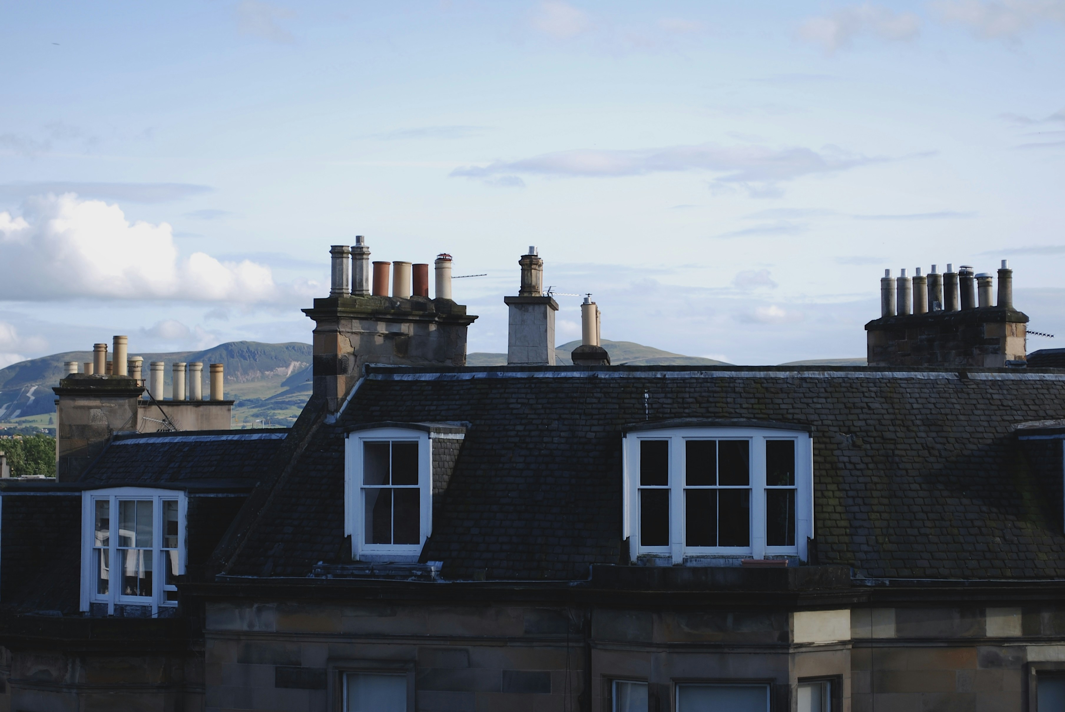 A collection of ornate chimneys atop a traditional building, framed by a clear blue sky with distant hills in the background.