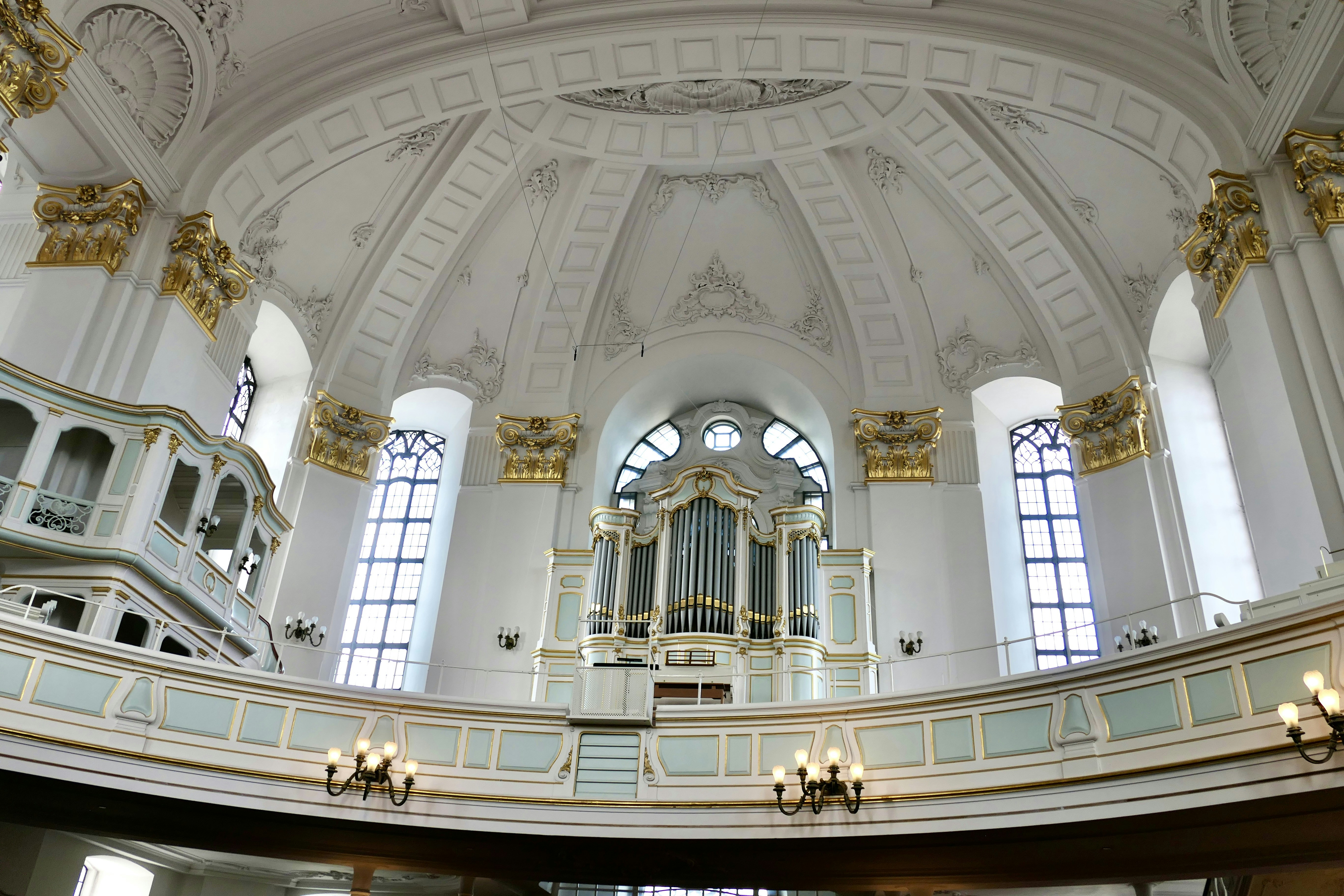 Interior of a grand church showcasing ornate architecture and a majestic pipe organ beneath a beautifully detailed ceiling.