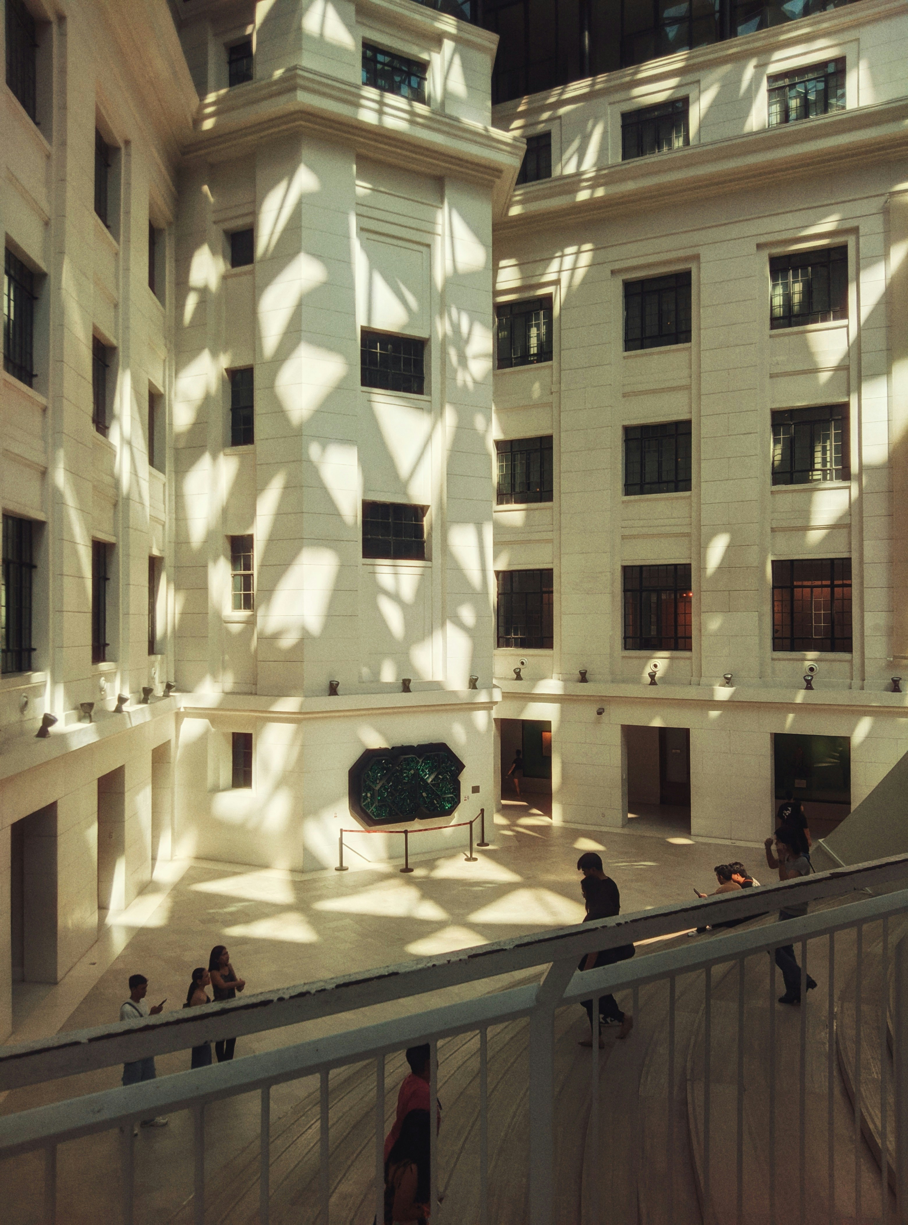 Intricate patterns of light cast across a modern architectural space, featuring a striking green sculpture amidst a minimalist design.