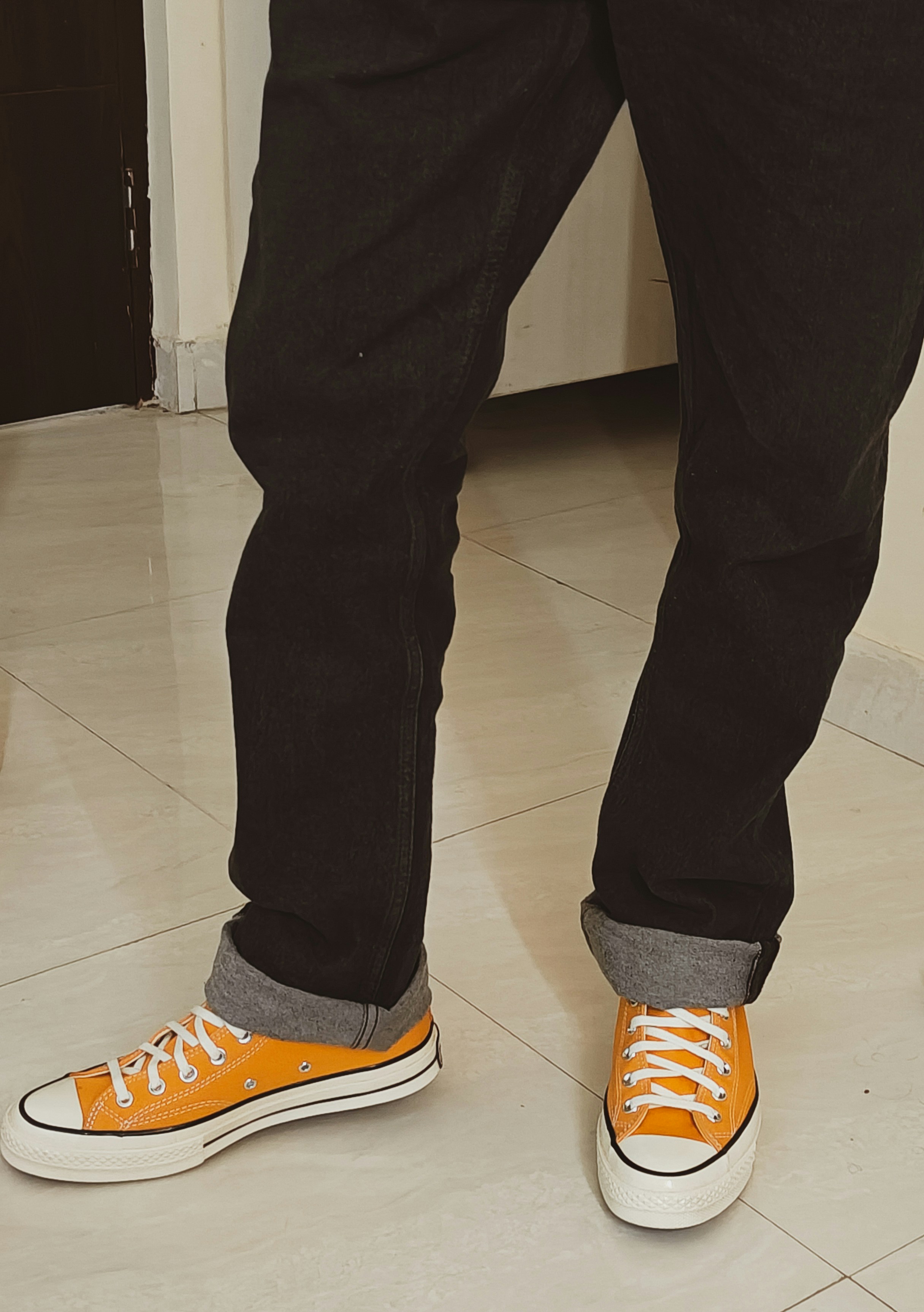In style | Person's legs wearing black jeans and orange sneakers.