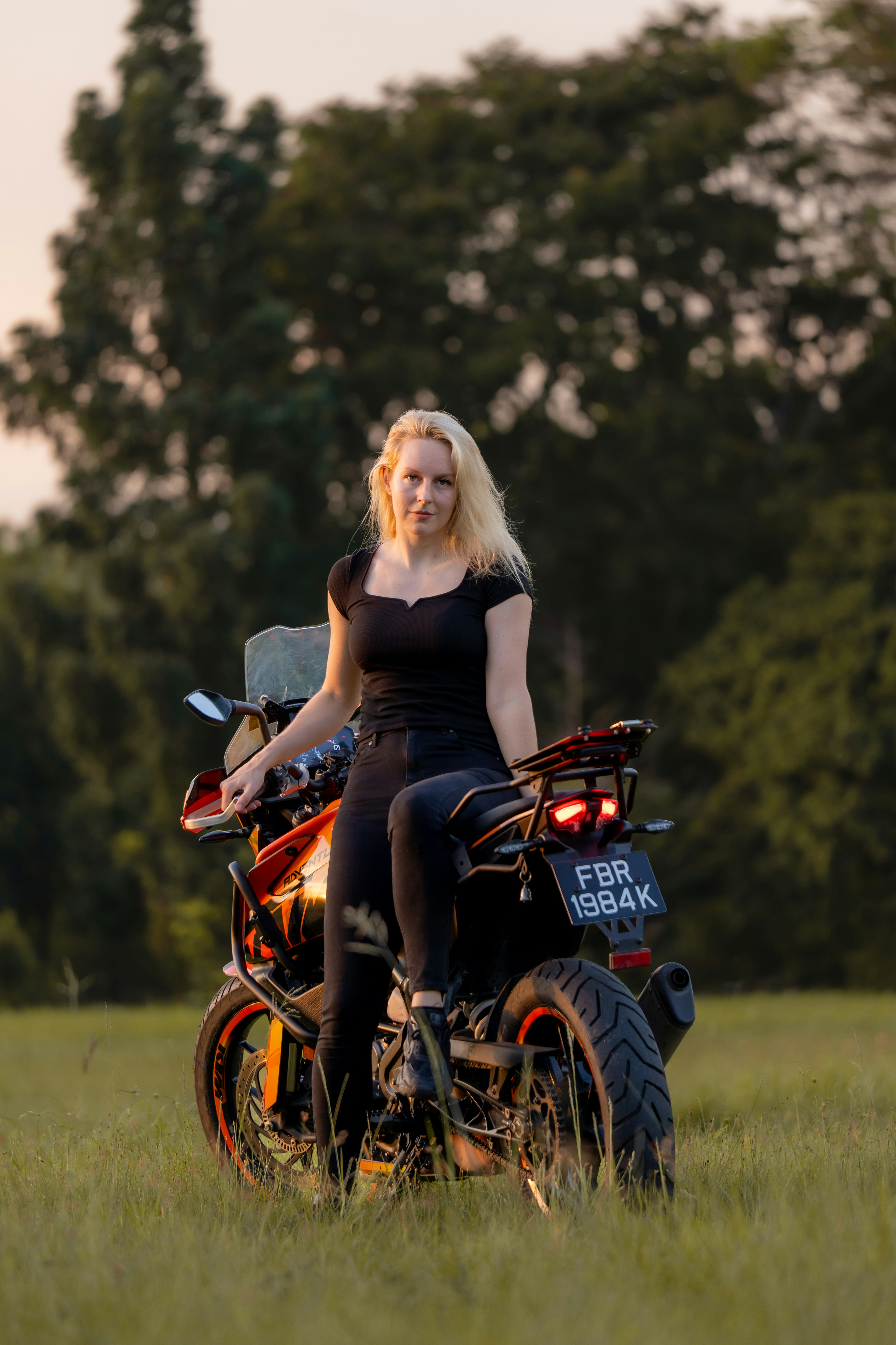 A woman poses on a motorcycle in a field.