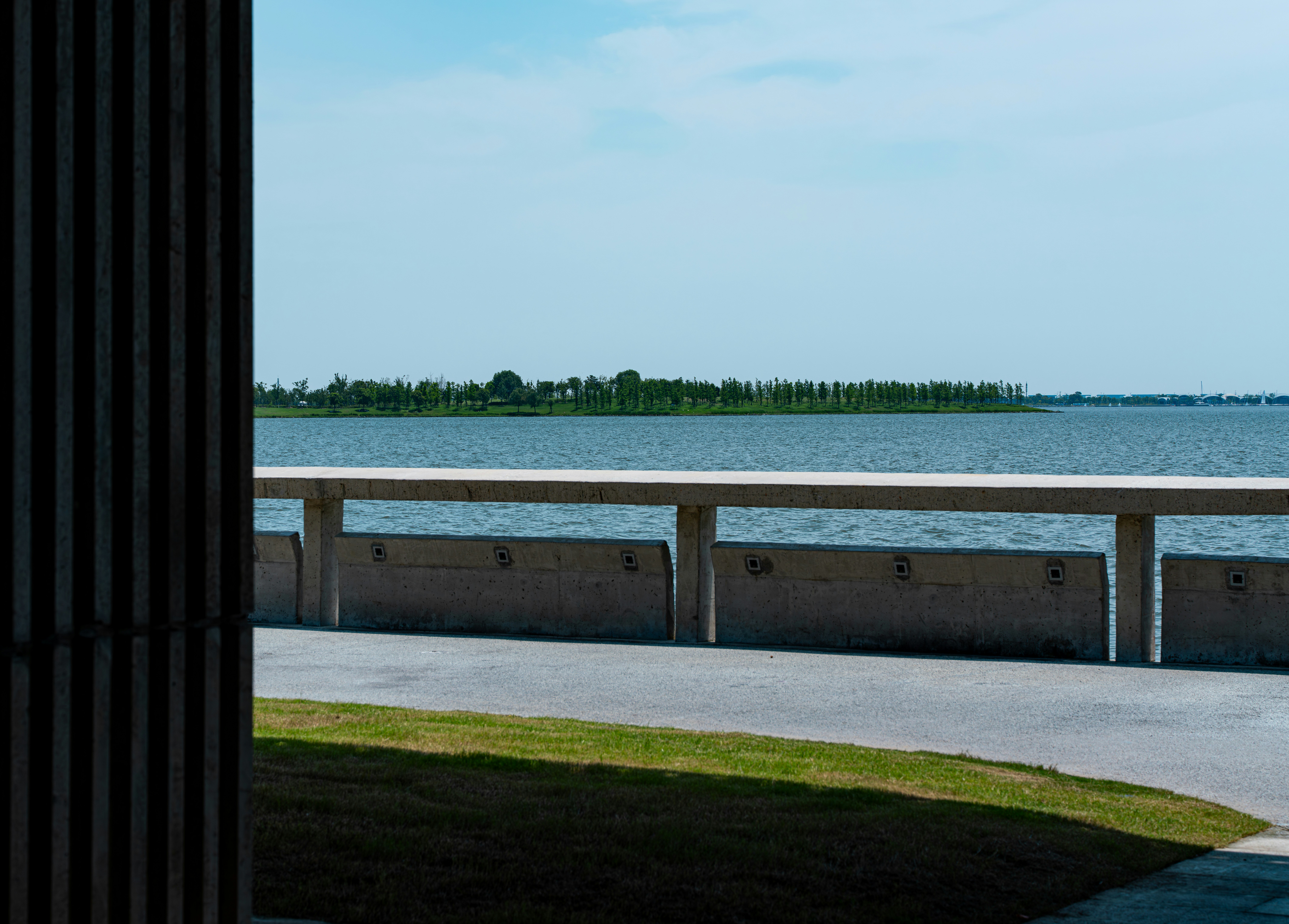 A tranquil lakeside view framed by a modern concrete structure, showcasing lush greenery along the water's edge.