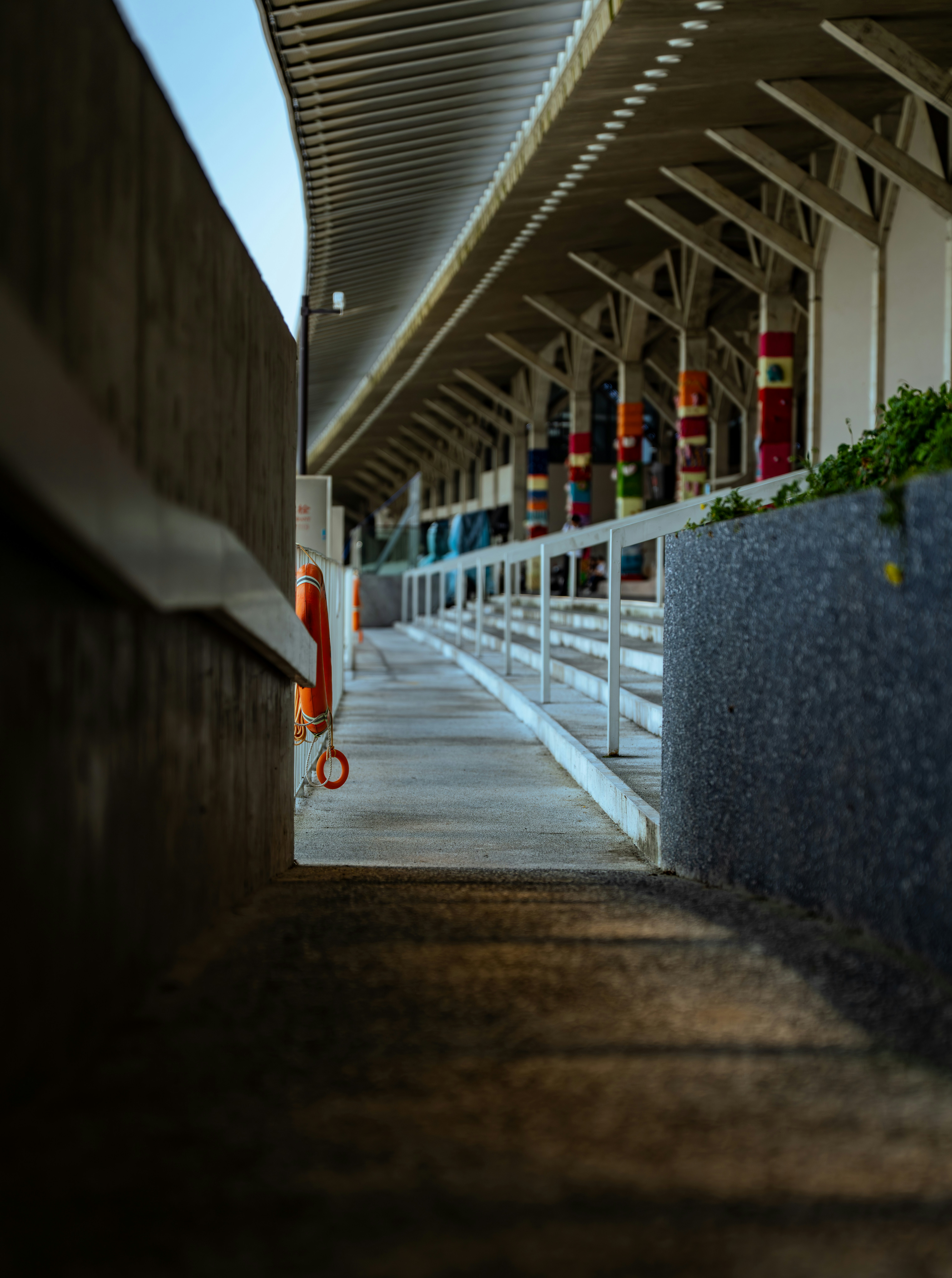 A winding walkway framed by colorful columns and a protective overhang, leading towards an inviting entrance.