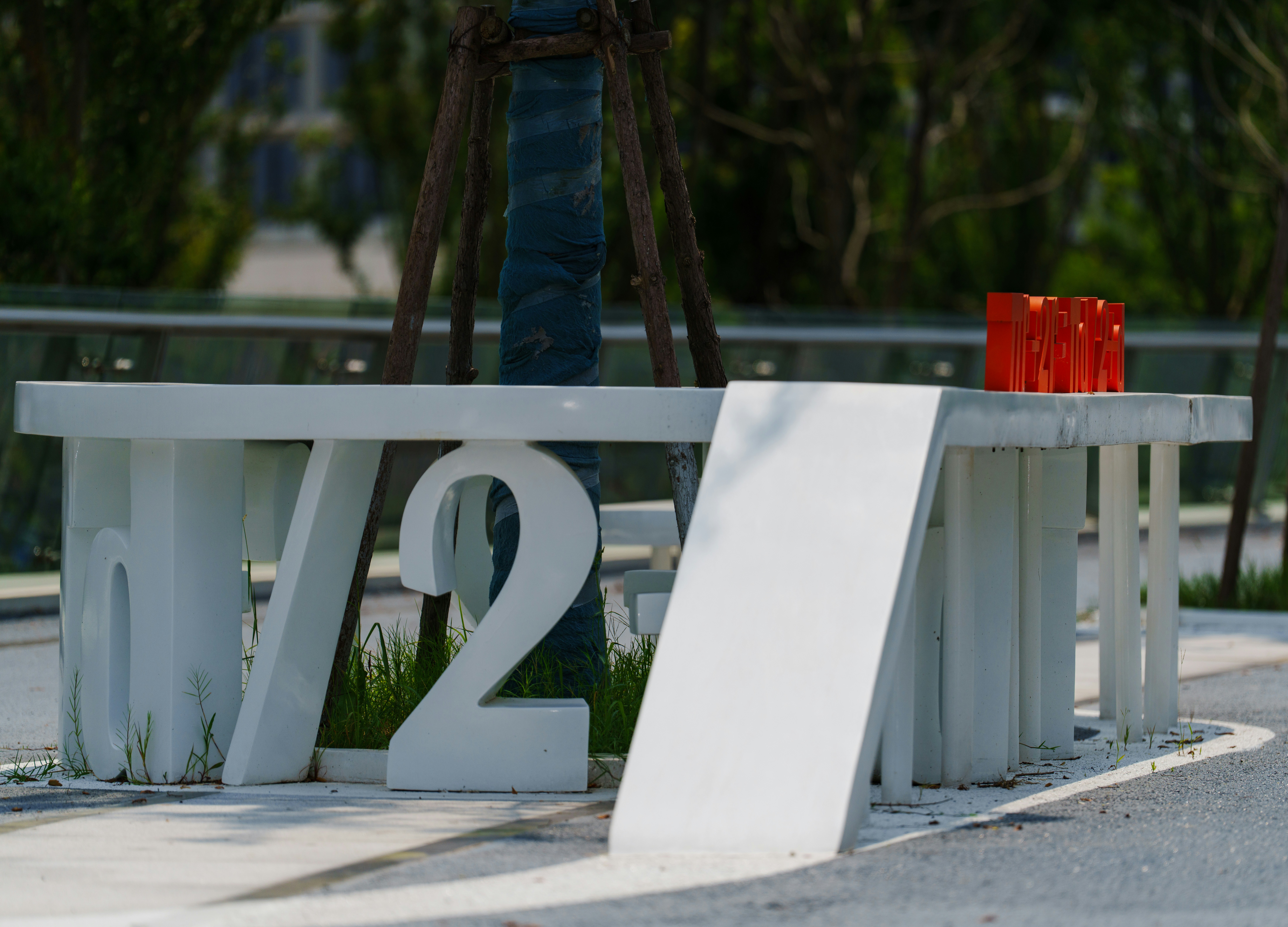 Contemporary white bench with bold numerals and vibrant orange accents, nestled among greenery in an urban setting.