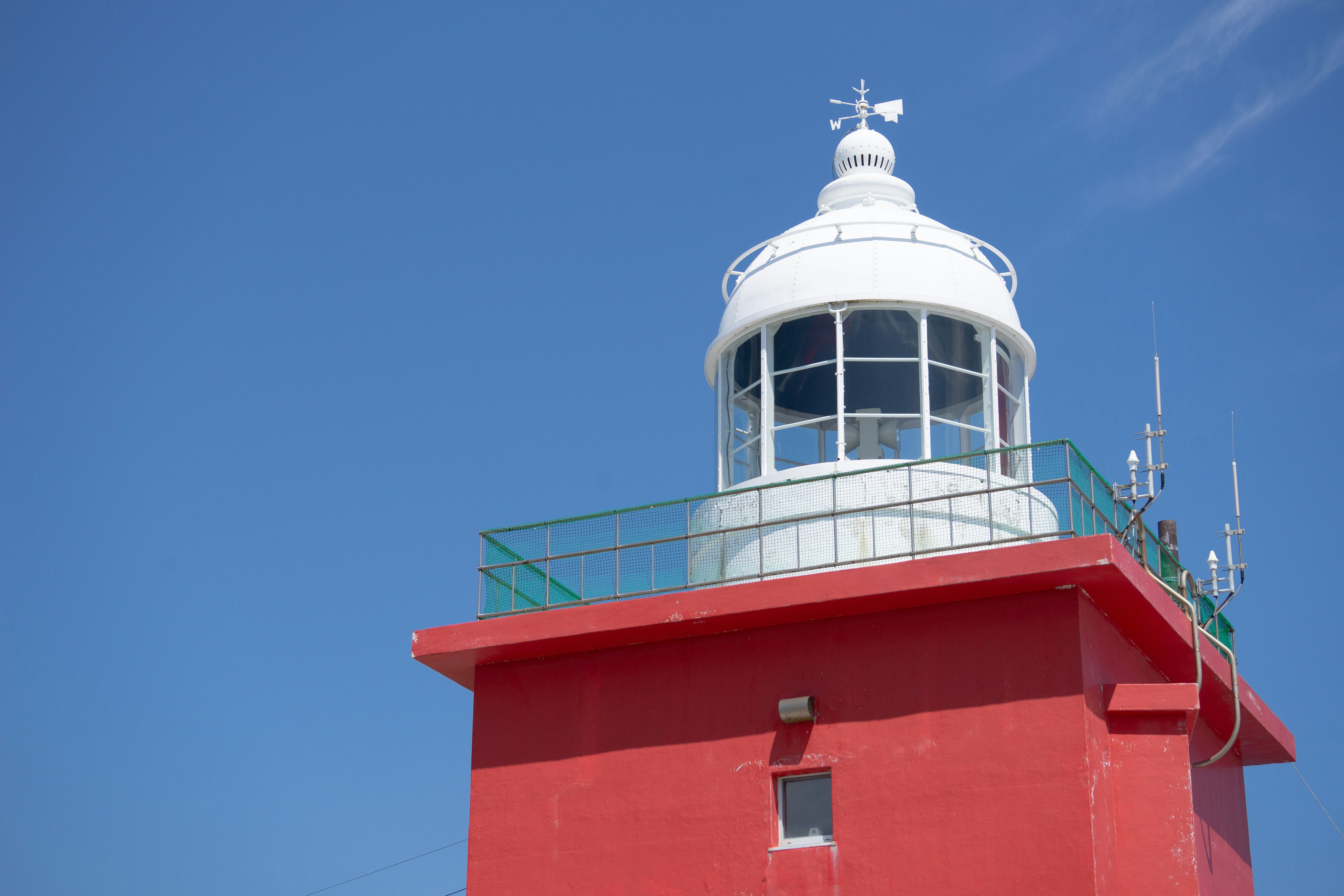 A bright red lighthouse with a glass observation dome stands against a clear blue sky, showcasing its role as a navigational aid.