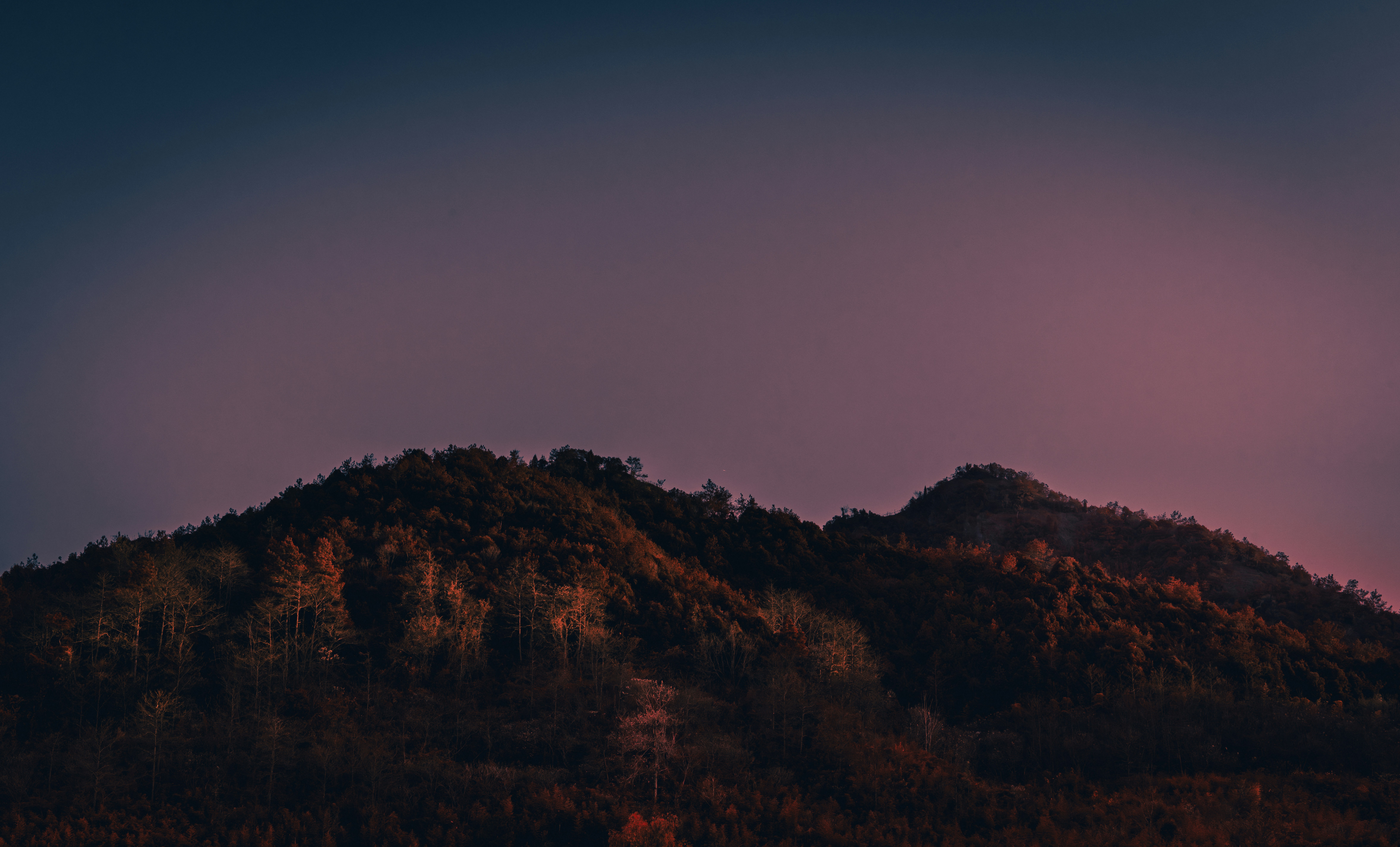 Silhouetted mountains under a twilight sky, showcasing a gradient of deep blues and purples with hints of autumn foliage. 