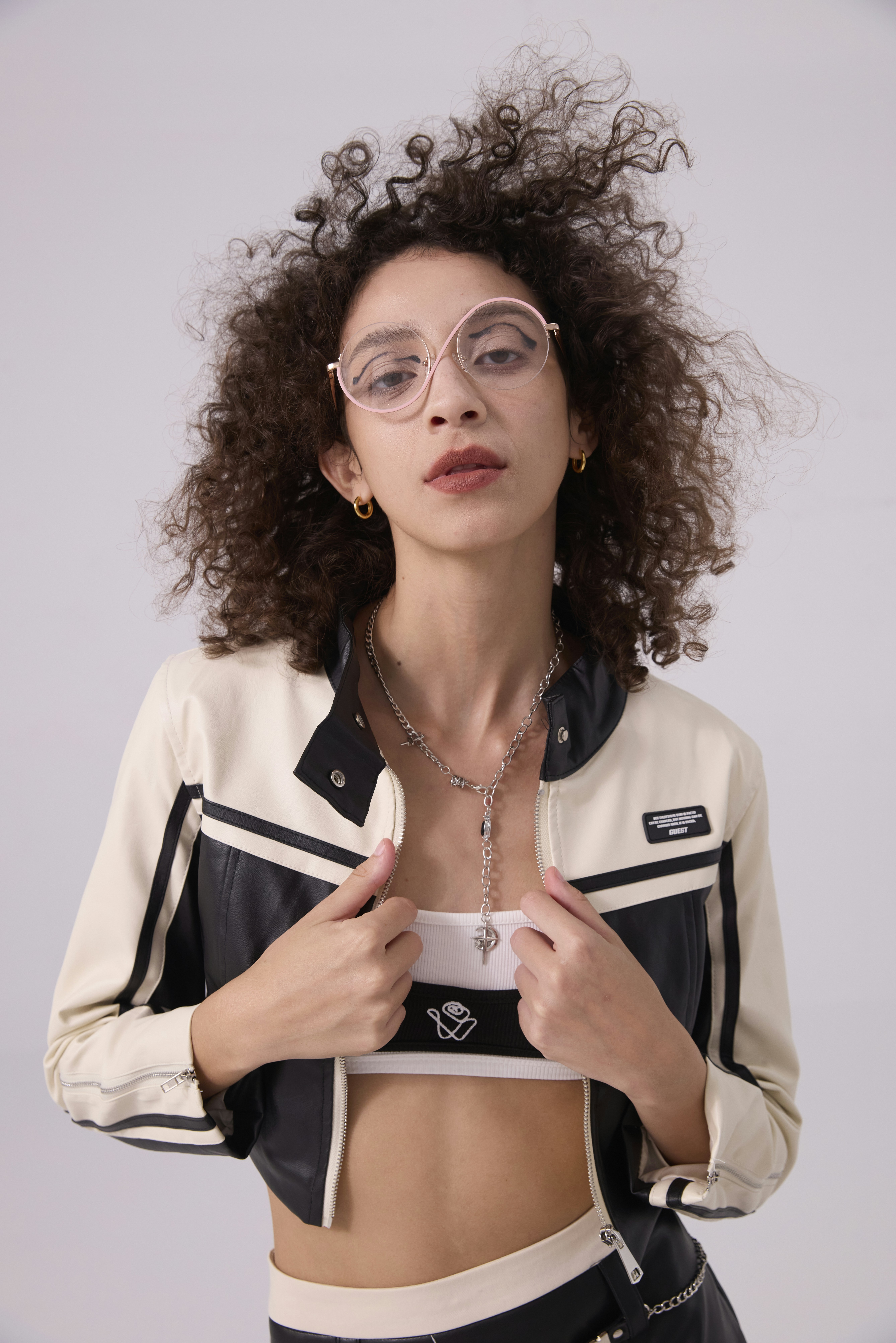 Model showcasing a contemporary outfit with a stylish jacket and accessories against a minimalist backdrop.