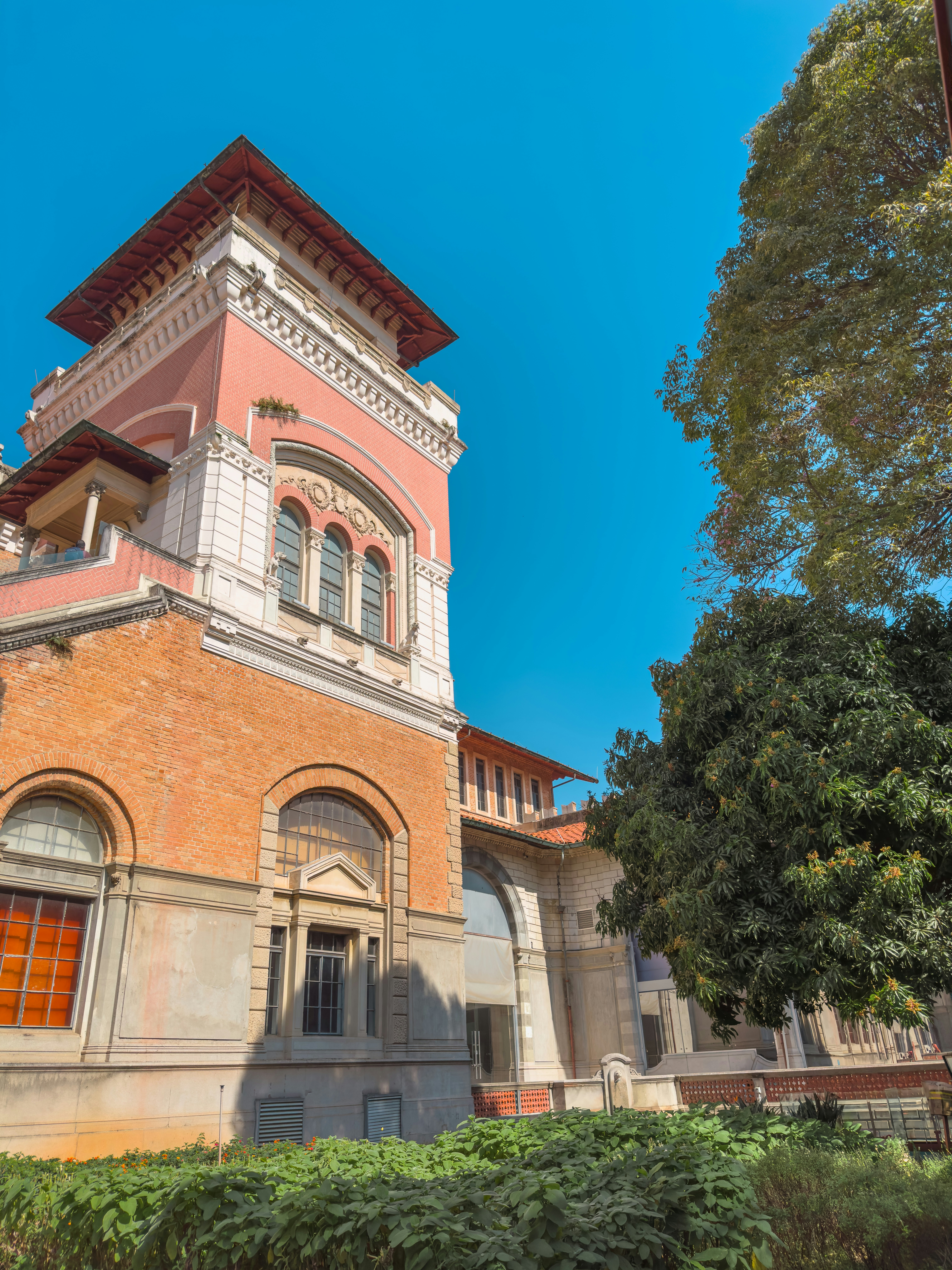 Historic building with ornate architecture framed by lush greenery under a clear blue sky.