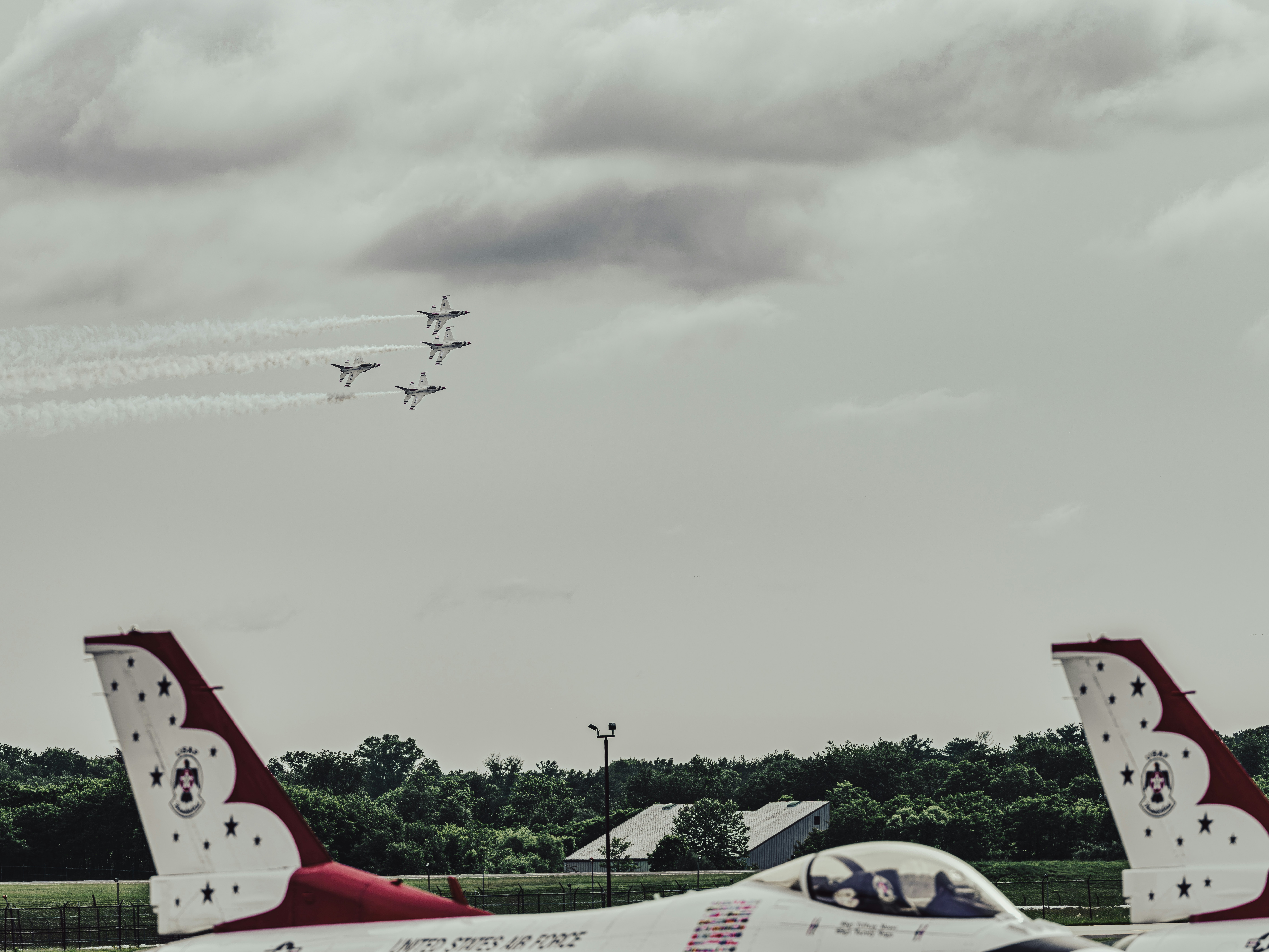 USAF Thunderbirds perform a four-ship diamond formation flyover above parked jets at McGuire AFB during the May 16th 2025 airshow in New Jersey. | Airplanes perform a formation flight over aircraft.