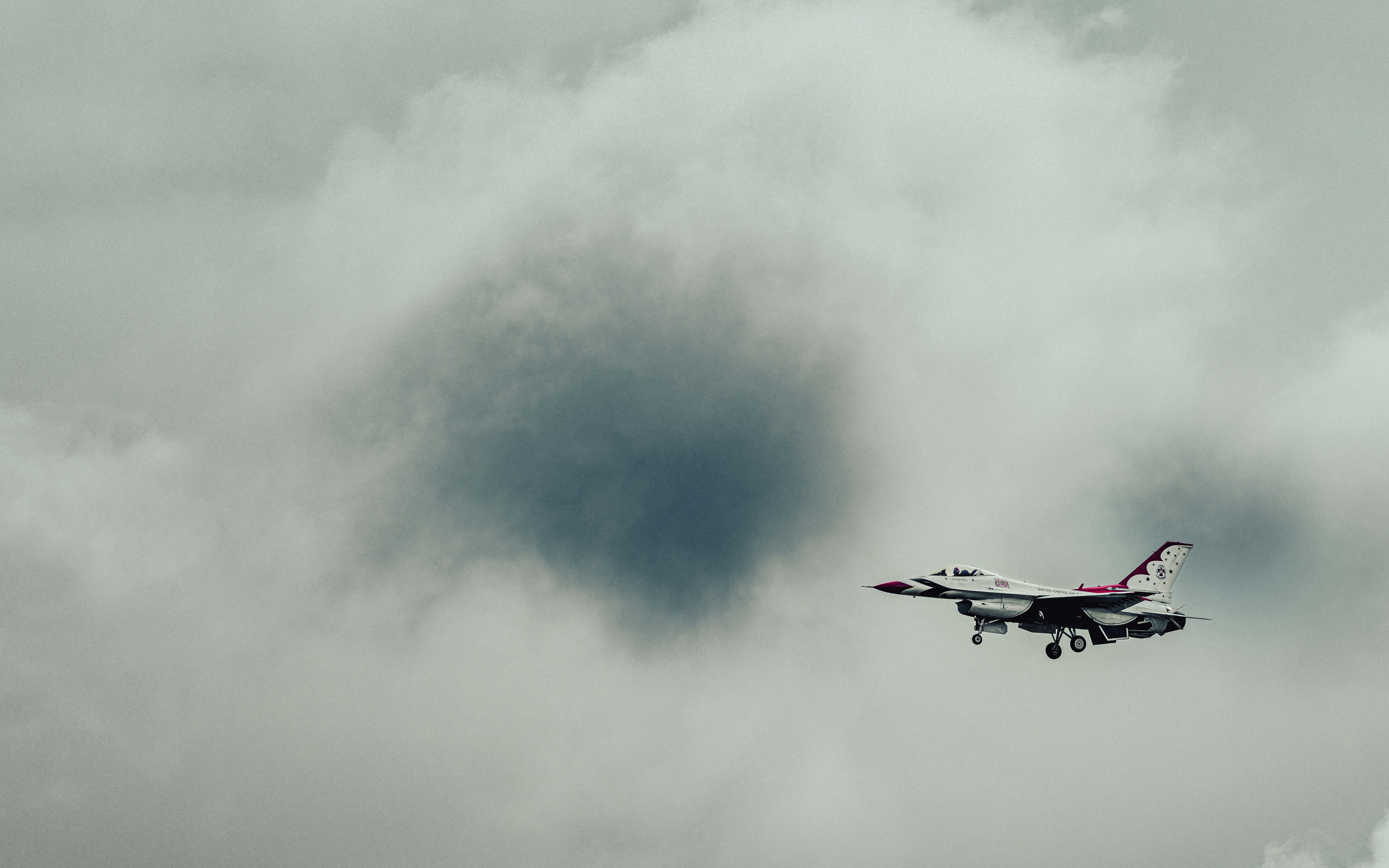 A USAF Thunderbird F-16 approaches landing under dramatic skies at McGuire AFB, New Jersey, during the May 16th 2025 airshow. Note the natural blue break in the cloud cover. | A fighter jet soars through cloudy skies.