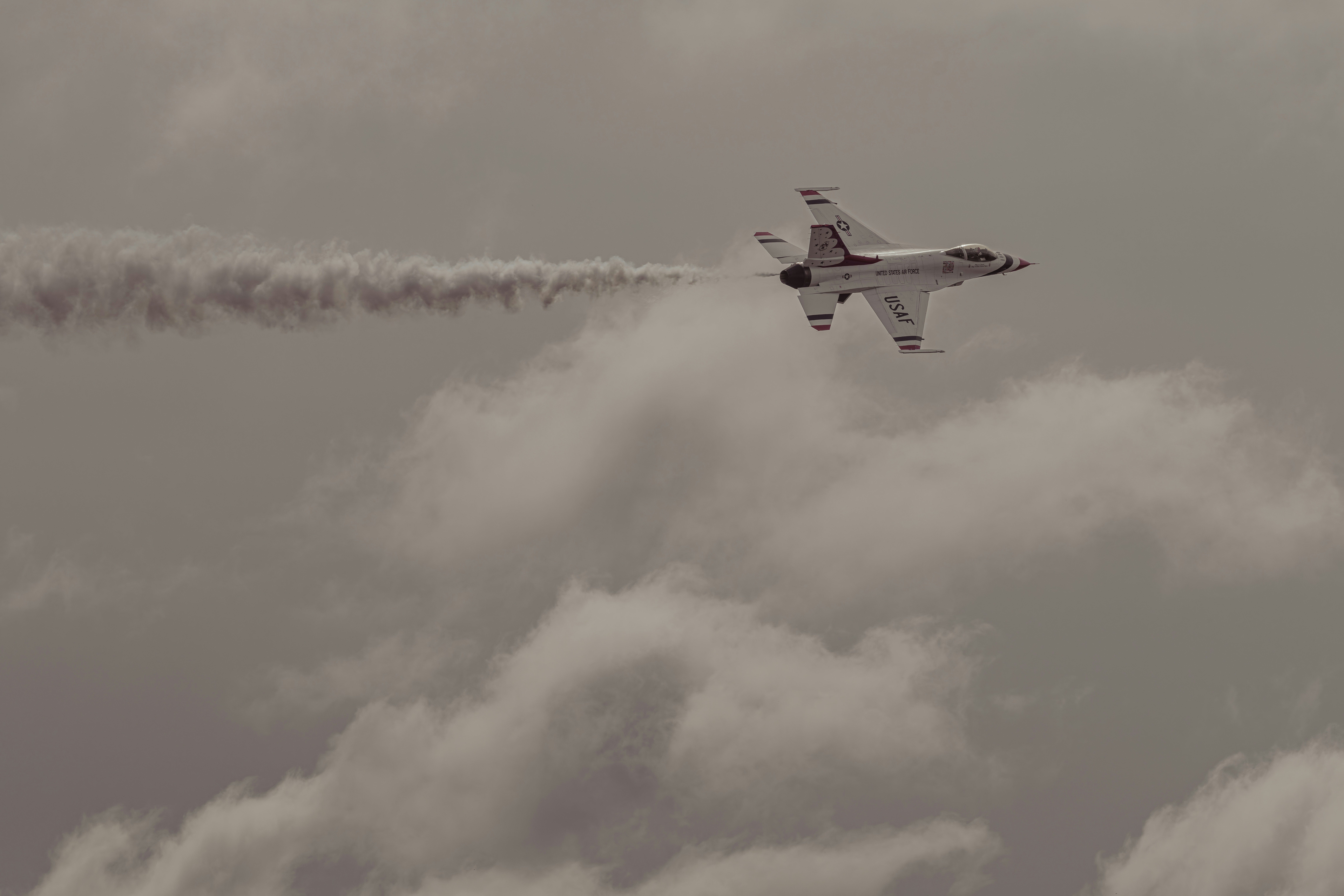 Fighter jet executing a sharp turn, leaving a trail of vapor against a backdrop of tumultuous clouds.