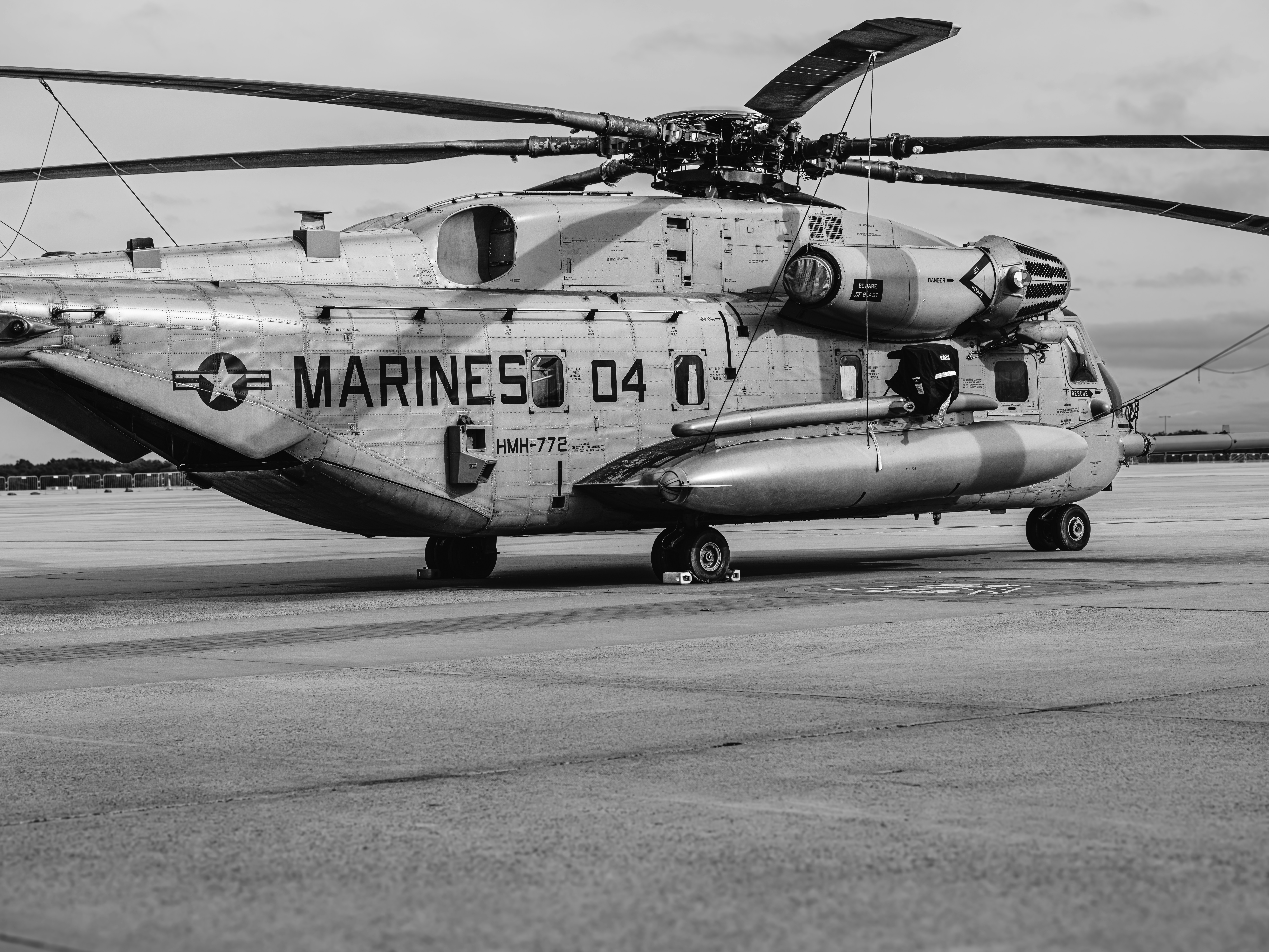 Black and white image of a USMC CH-53E Super Stallion from HMH-772 at McGuire AFB, New Jersey, May 2025. Side view on static display. | A large marine helicopter on the ground.