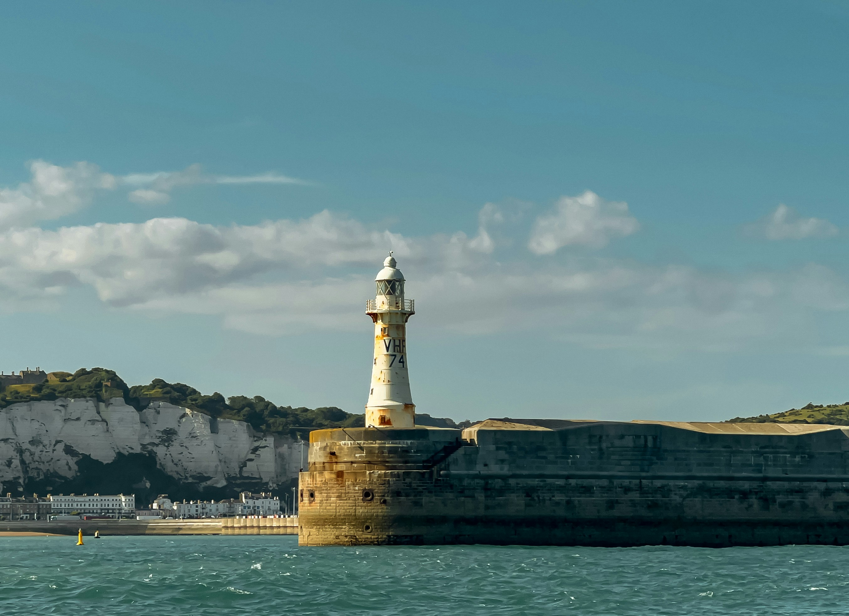 Beacon on the Breakwater: A Sunlit Lighthouse Over a Quiet Harbor