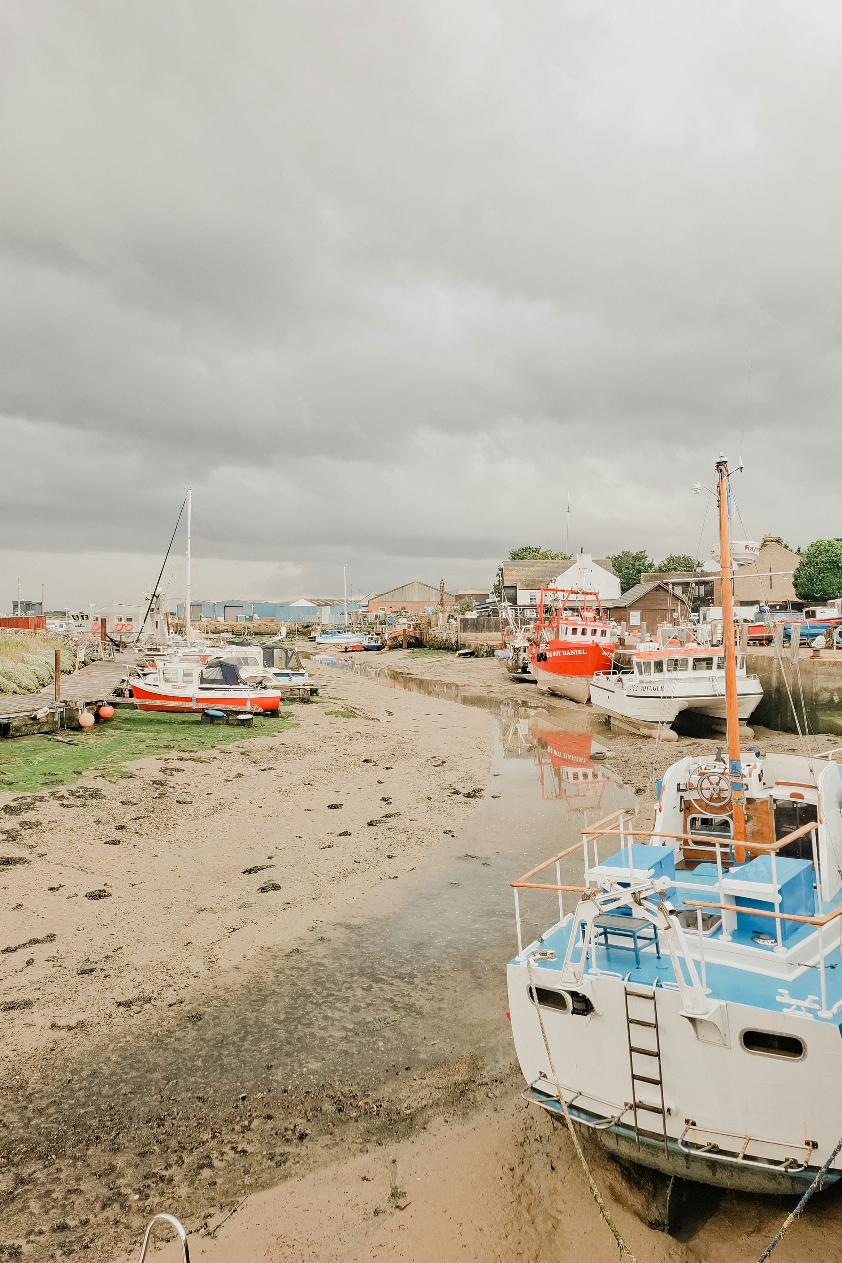 Boats are stranded in a muddy harbor on a cloudy day.