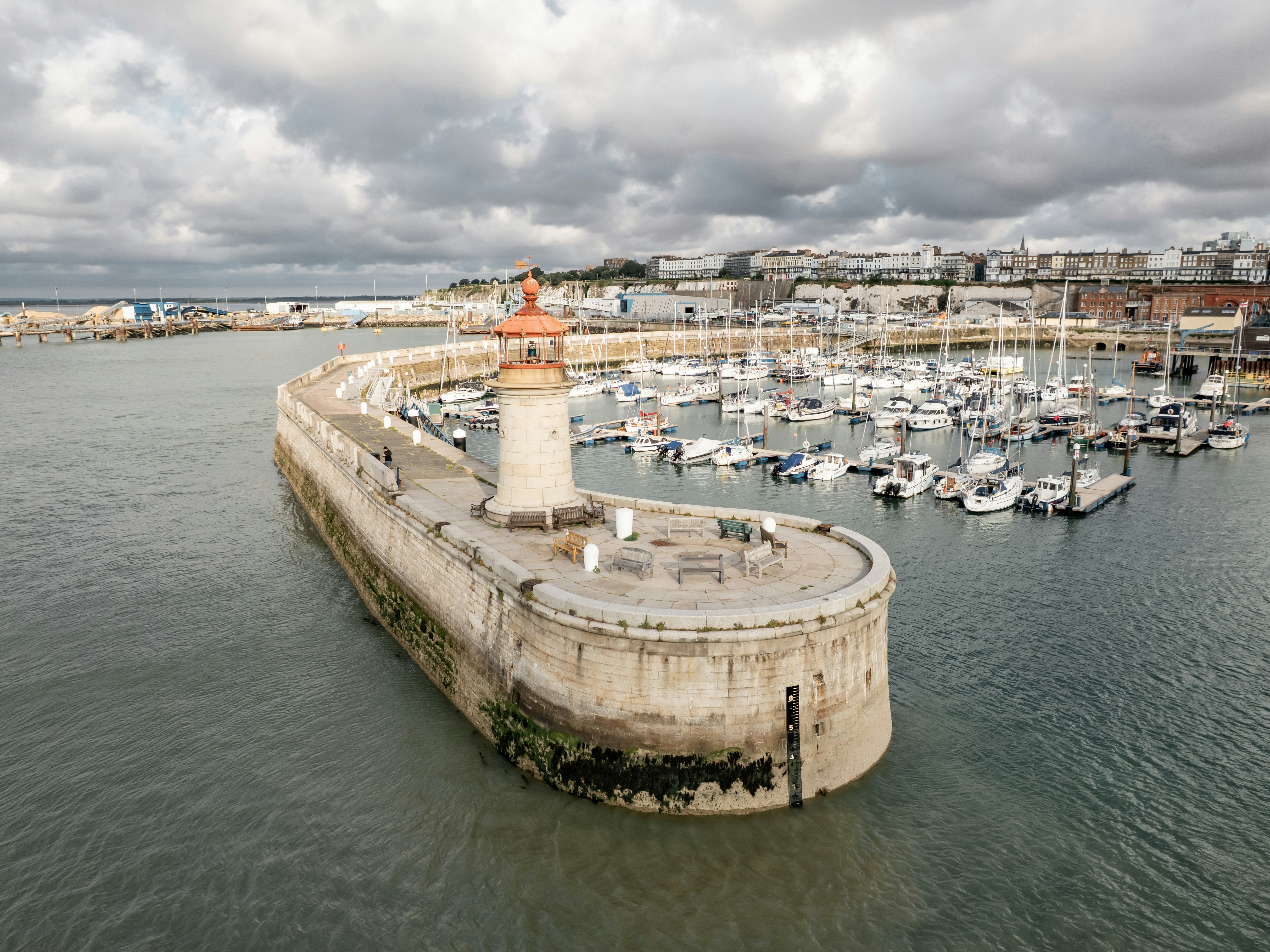 A lighthouse stands guard over a bustling marina, surrounded by boats and a picturesque waterfront. The scene captures the essence of coastal life.