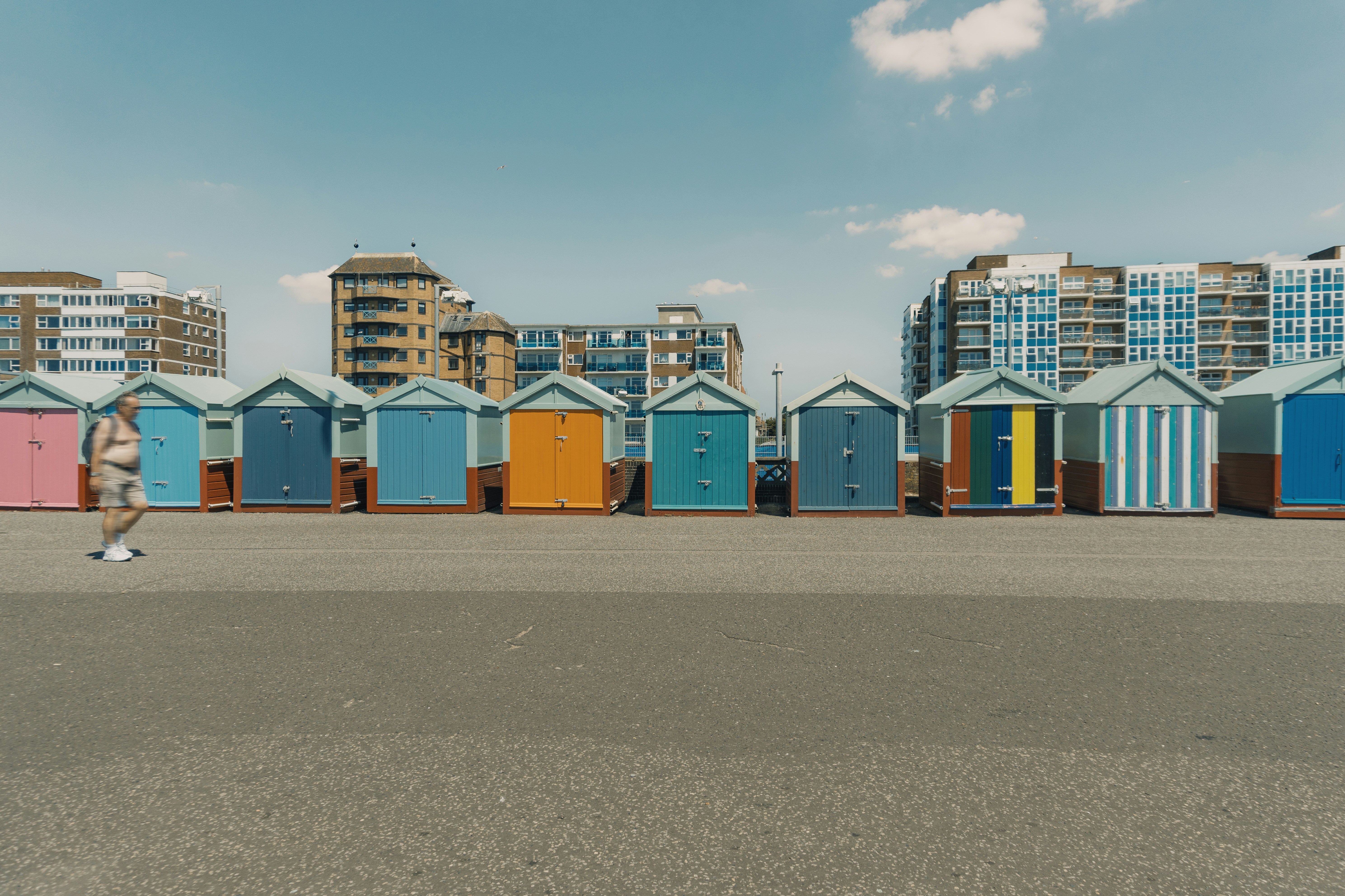 Vibrant beach huts lined along a promenade, with a pedestrian strolling by. The scene captures the essence of seaside leisure.
