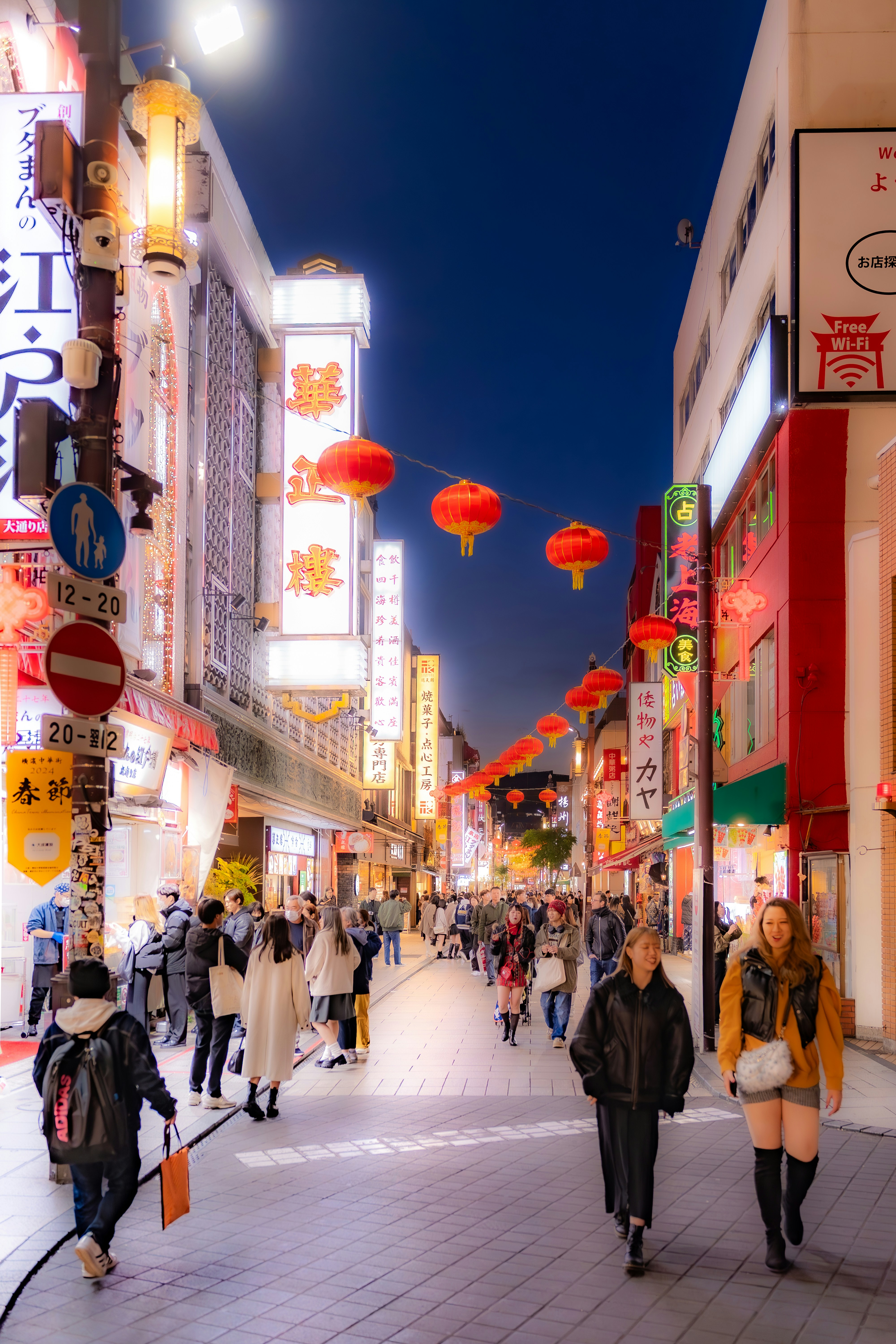 Bustling street scene filled with pedestrians in a vibrant city adorned with glowing lanterns and neon signs. The lively atmosphere captures the essence of urban nightlife.