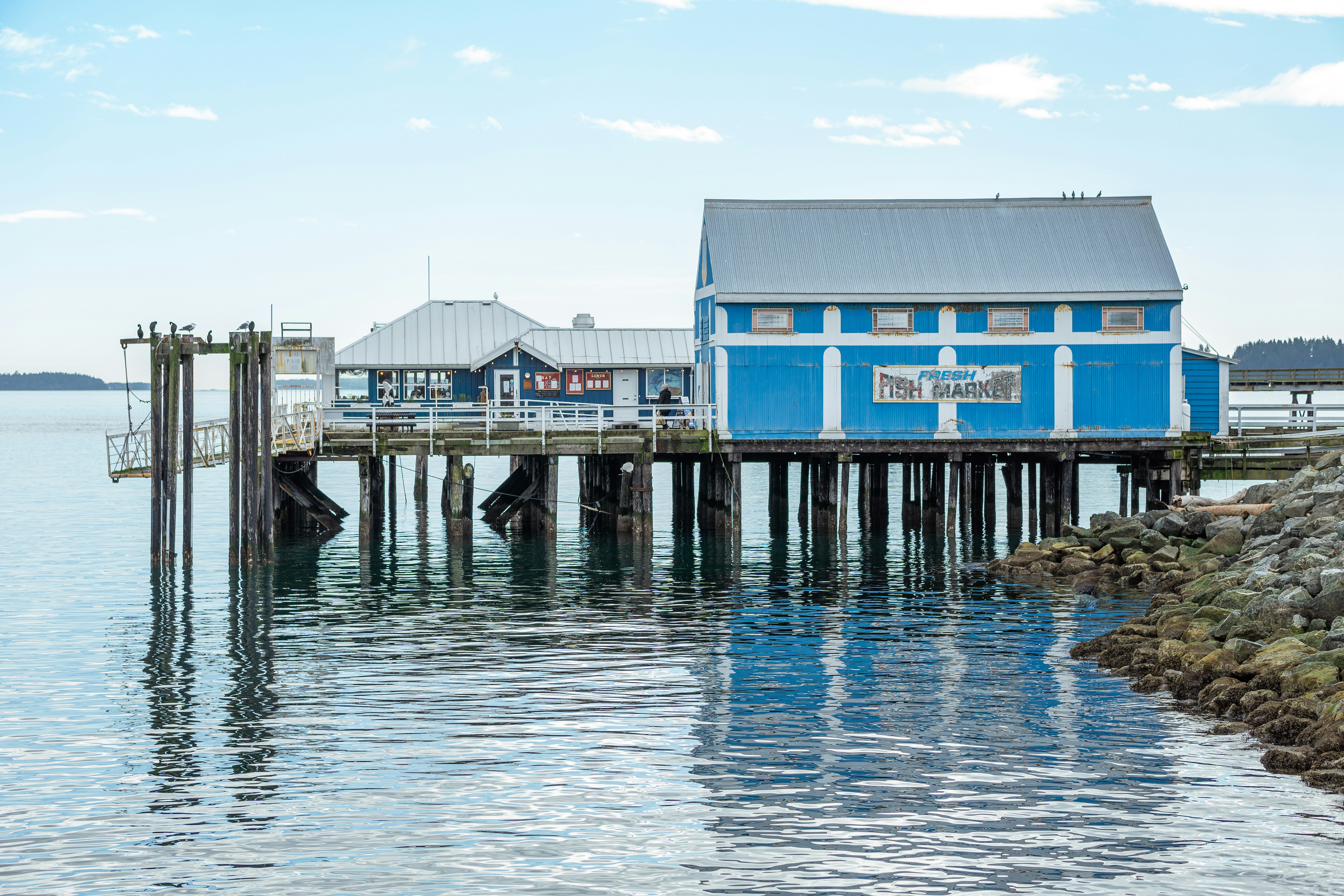 A blue building on a pier reflected in calm water.