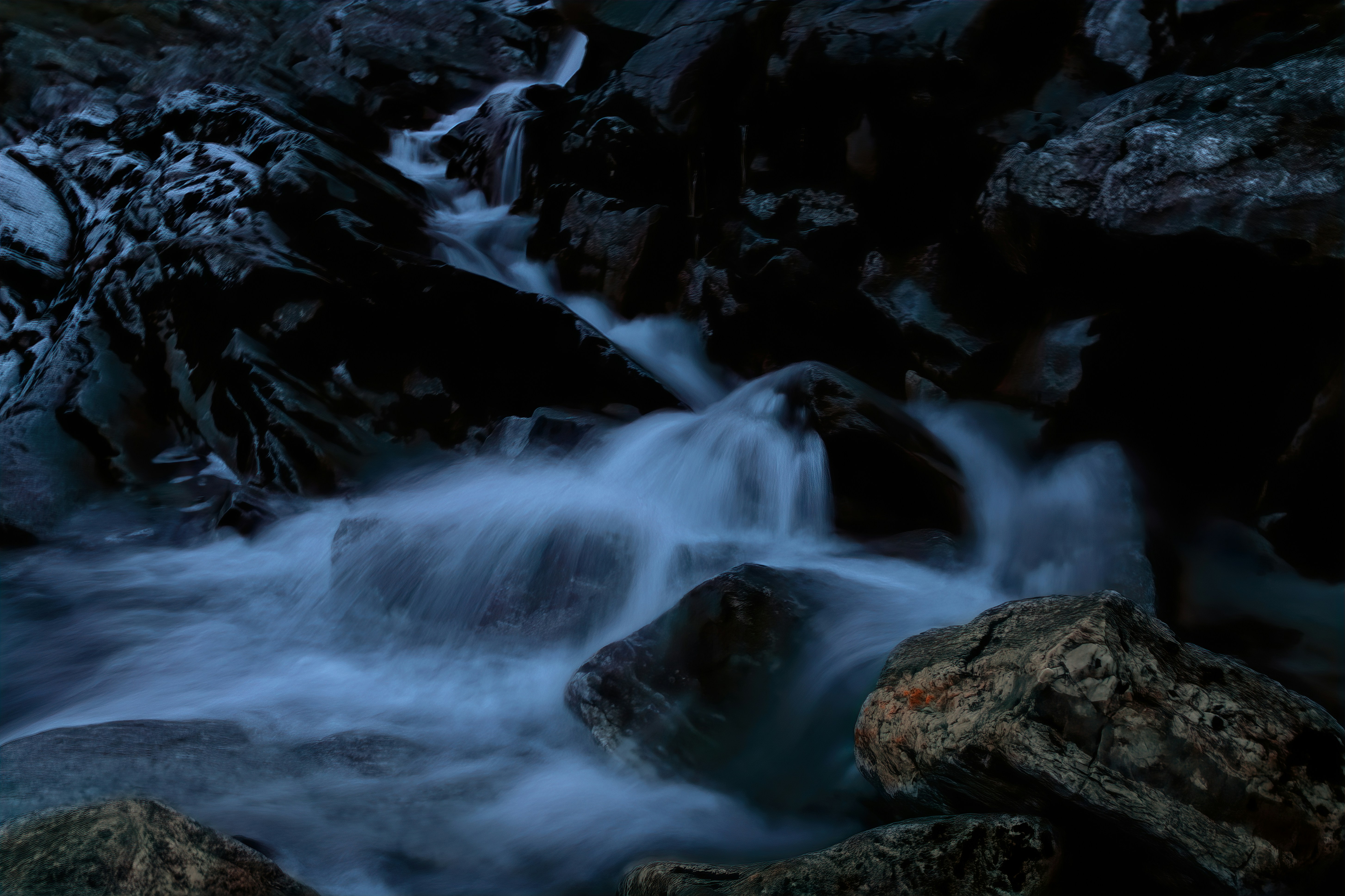Gentle water cascades over smooth rocks in a serene, dimly lit environment, creating a tranquil atmosphere.