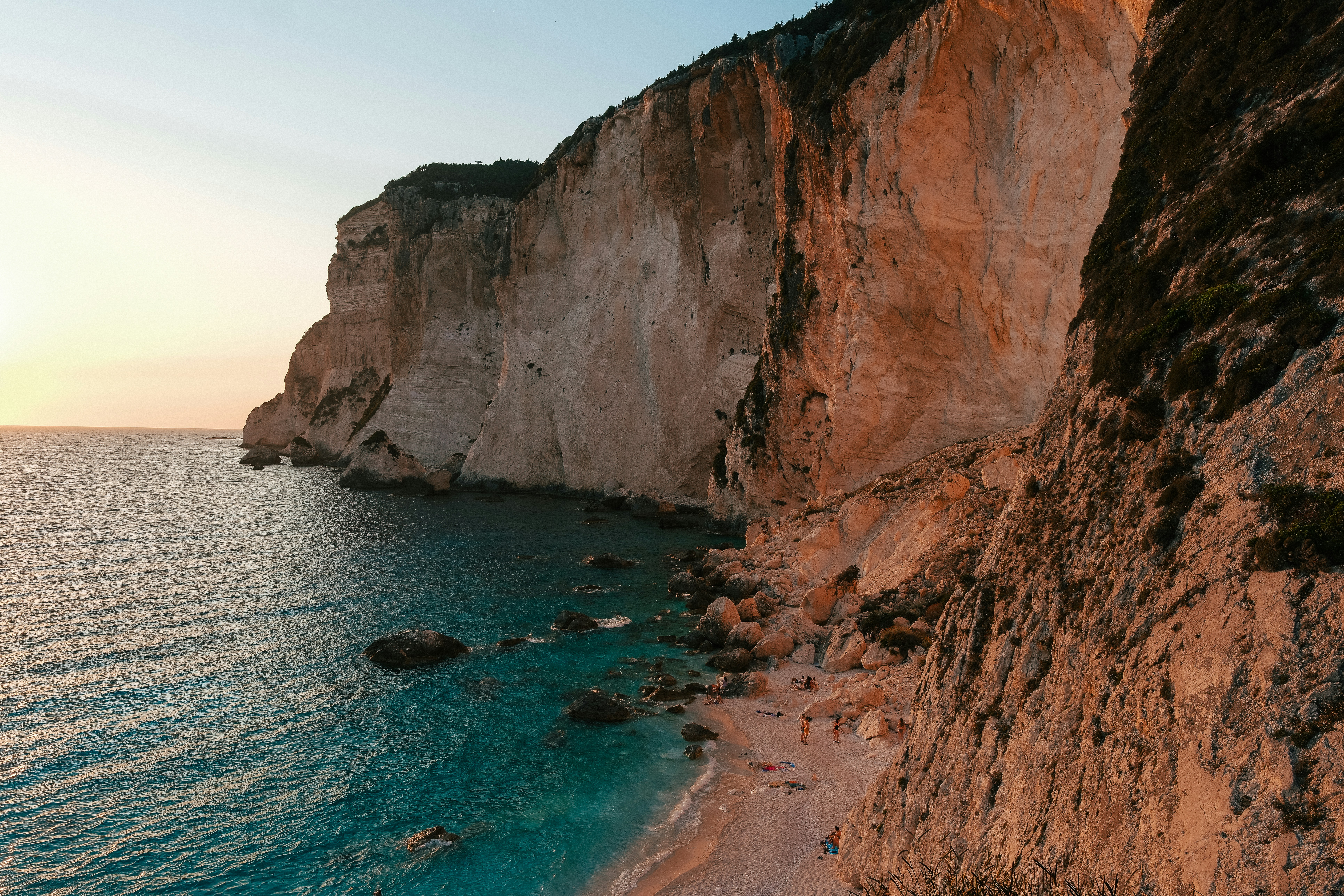 Cliffs meet the turquoise ocean under a sunset.