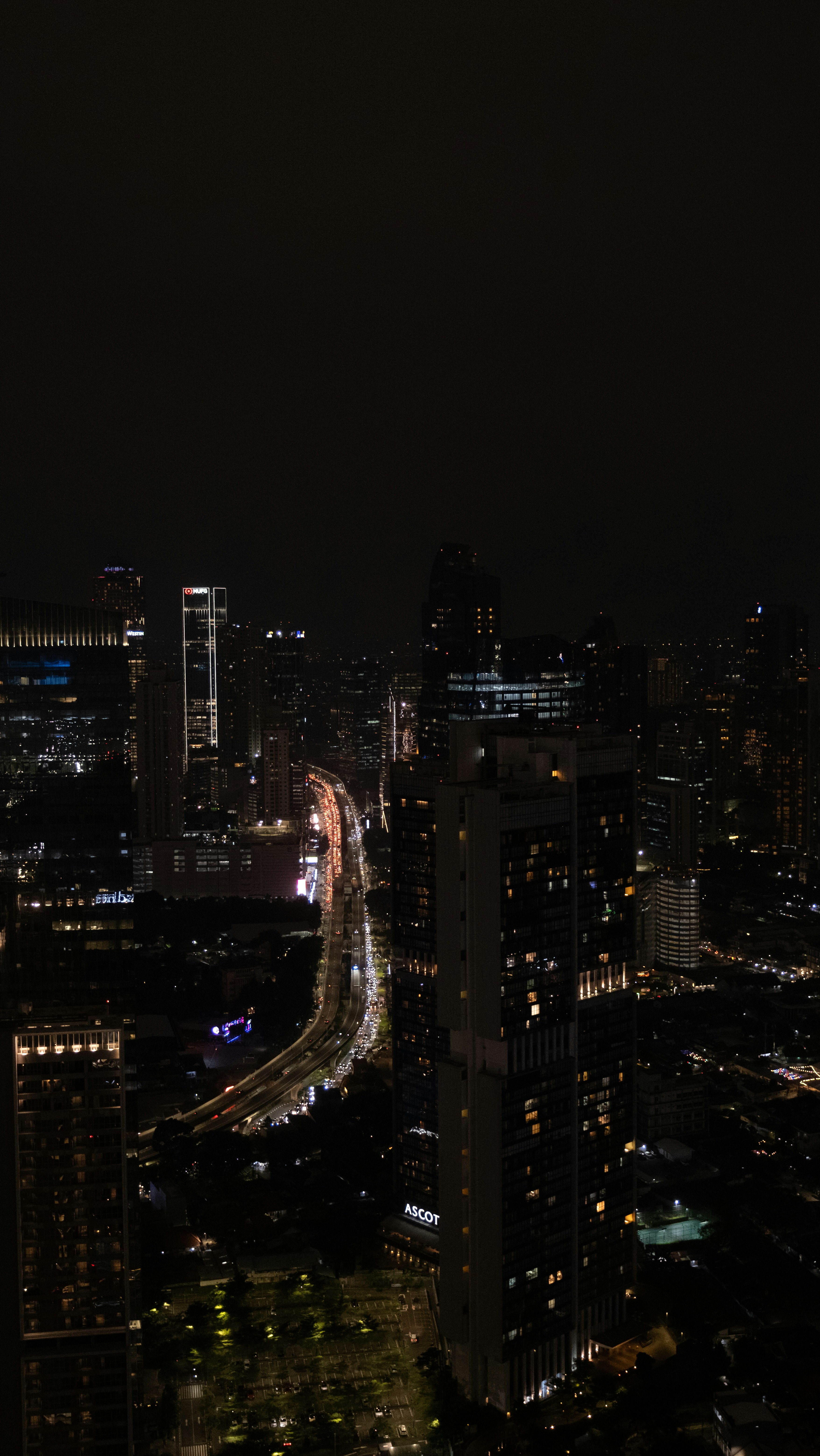 Vibrant city skyline illuminated at night, showcasing a busy road lined with glowing buildings. The scene captures the dynamic energy of urban life after dark.