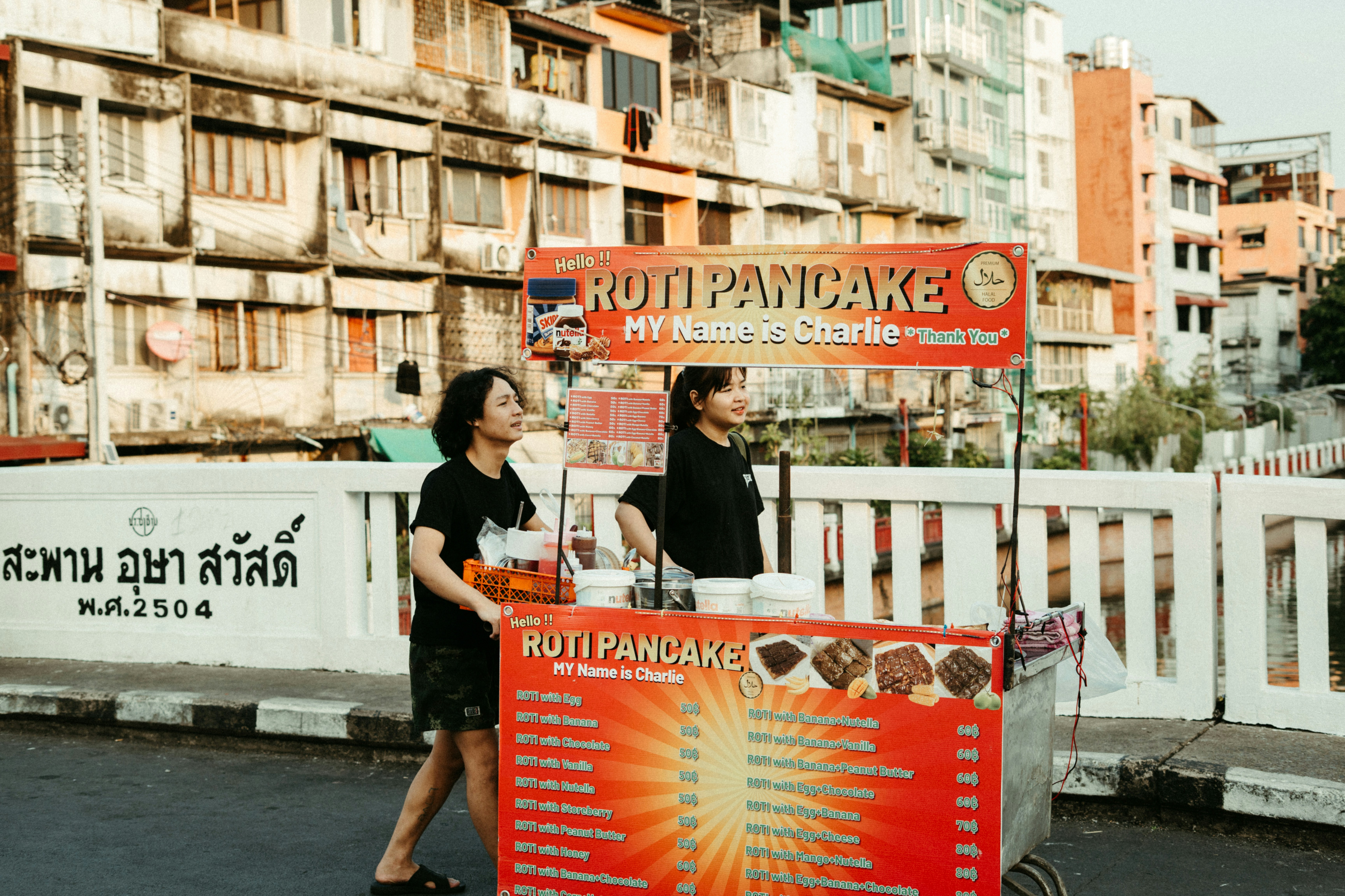 Two people operate a roti pancake street food cart.