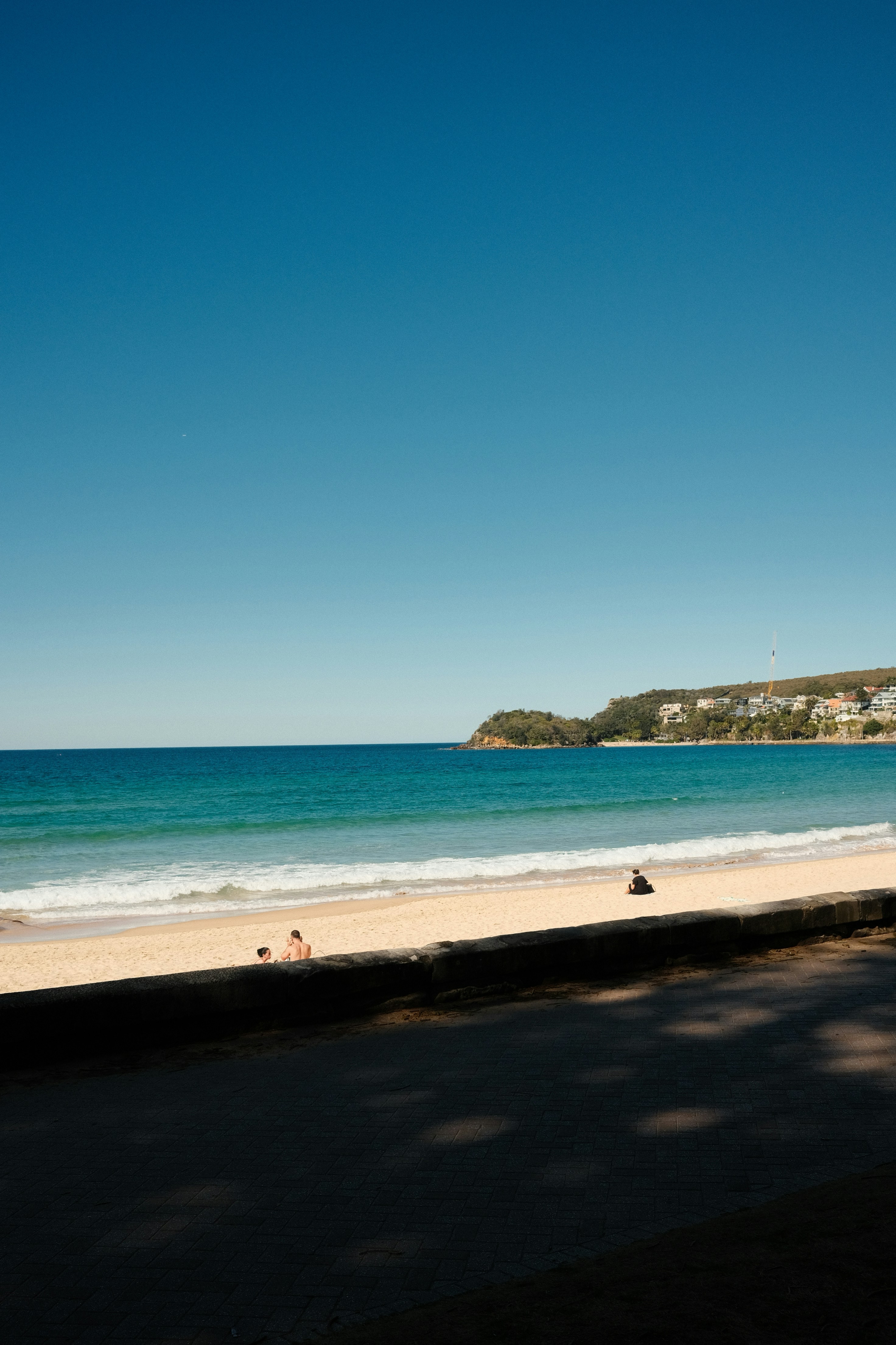 Two beachgoers enjoying the sun on a sandy shore, with gentle waves lapping at the beach under a clear blue sky.