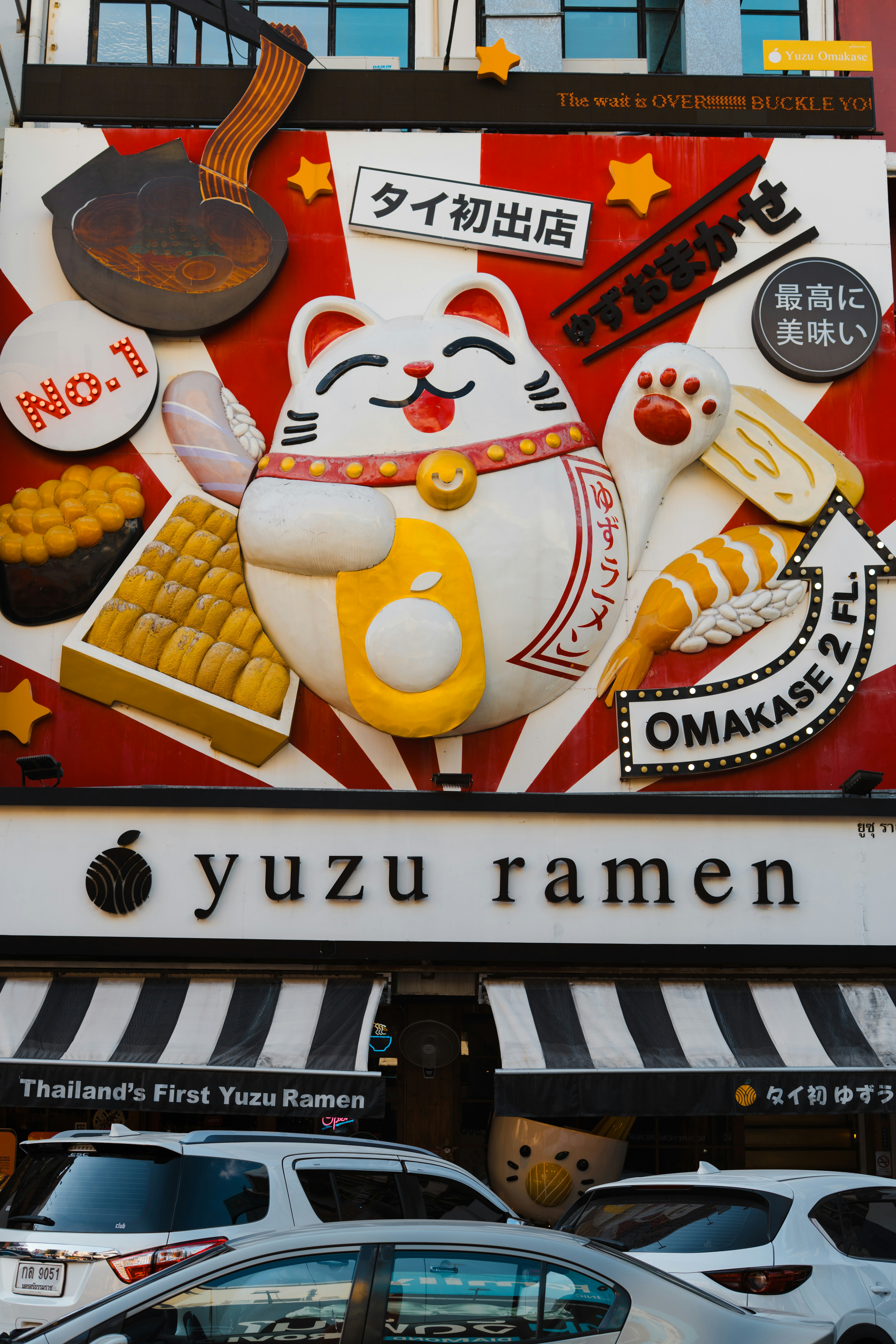 Colorful 3D sign featuring a smiling cat mascot and various ramen dishes, promoting Yuzu Ramen in Thailand. The vibrant design invites diners to experience Japanese cuisine.