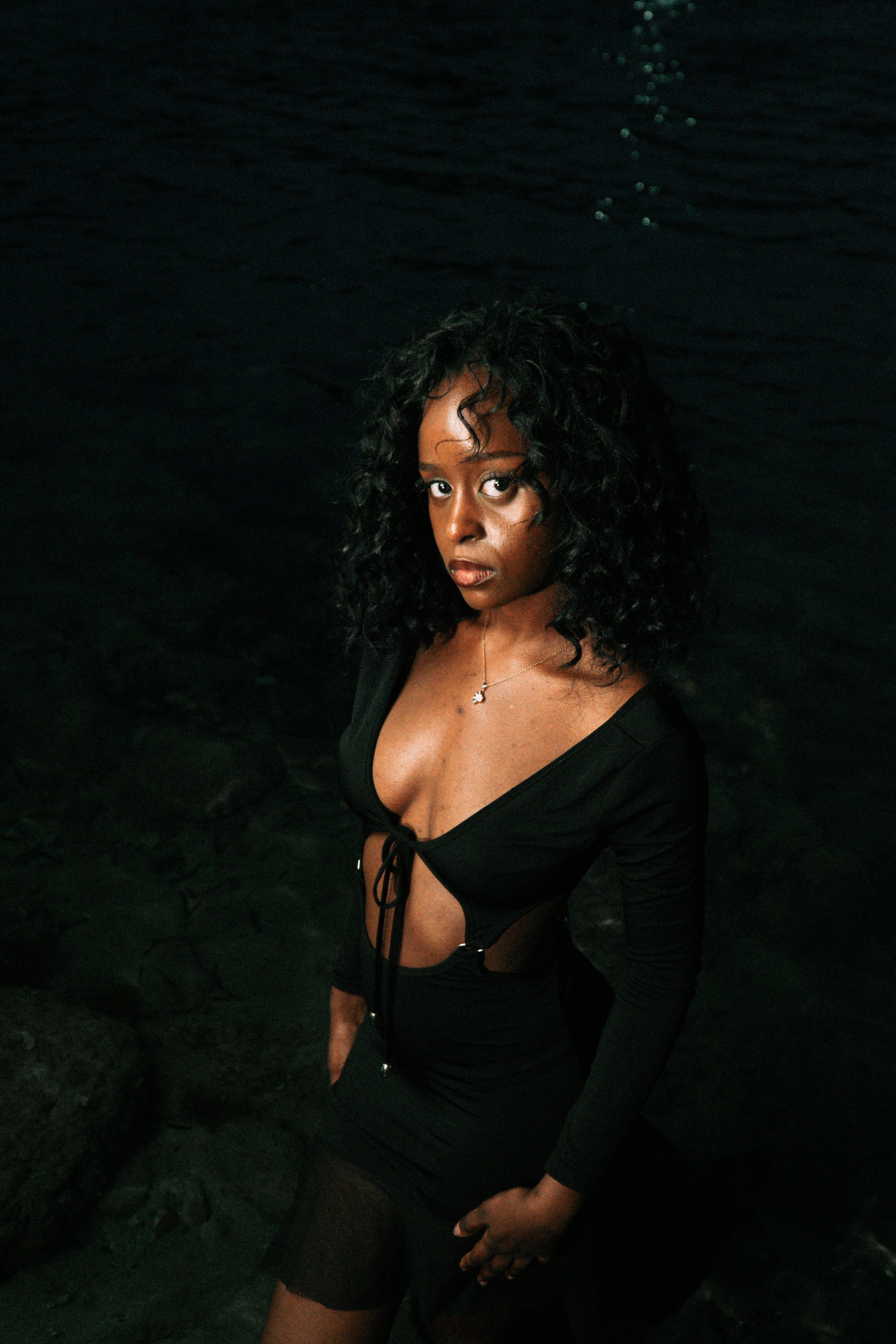Woman in a black dress poses near water.