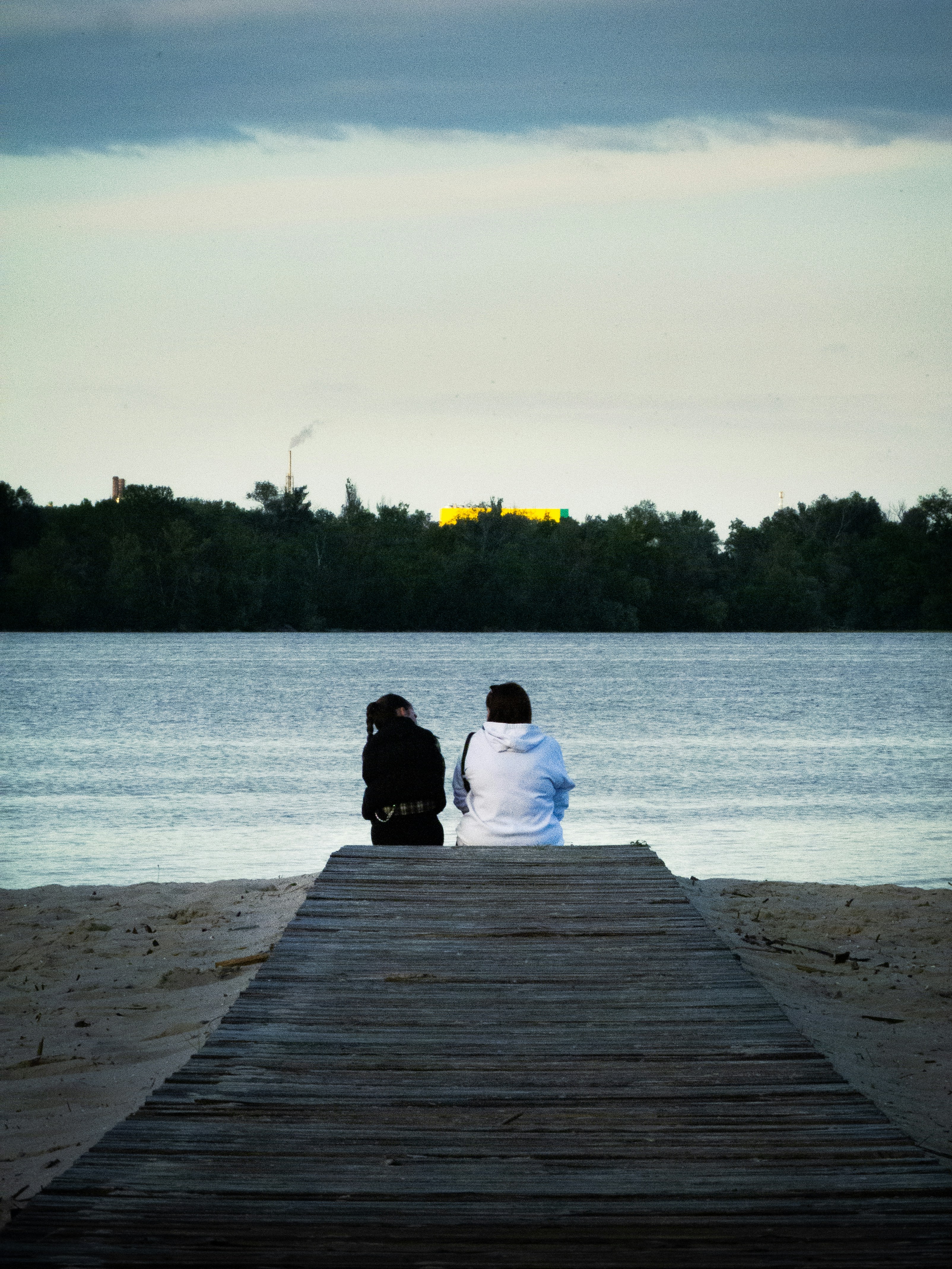 mom and daughter talks. | Two people sit on a dock overlooking the water.