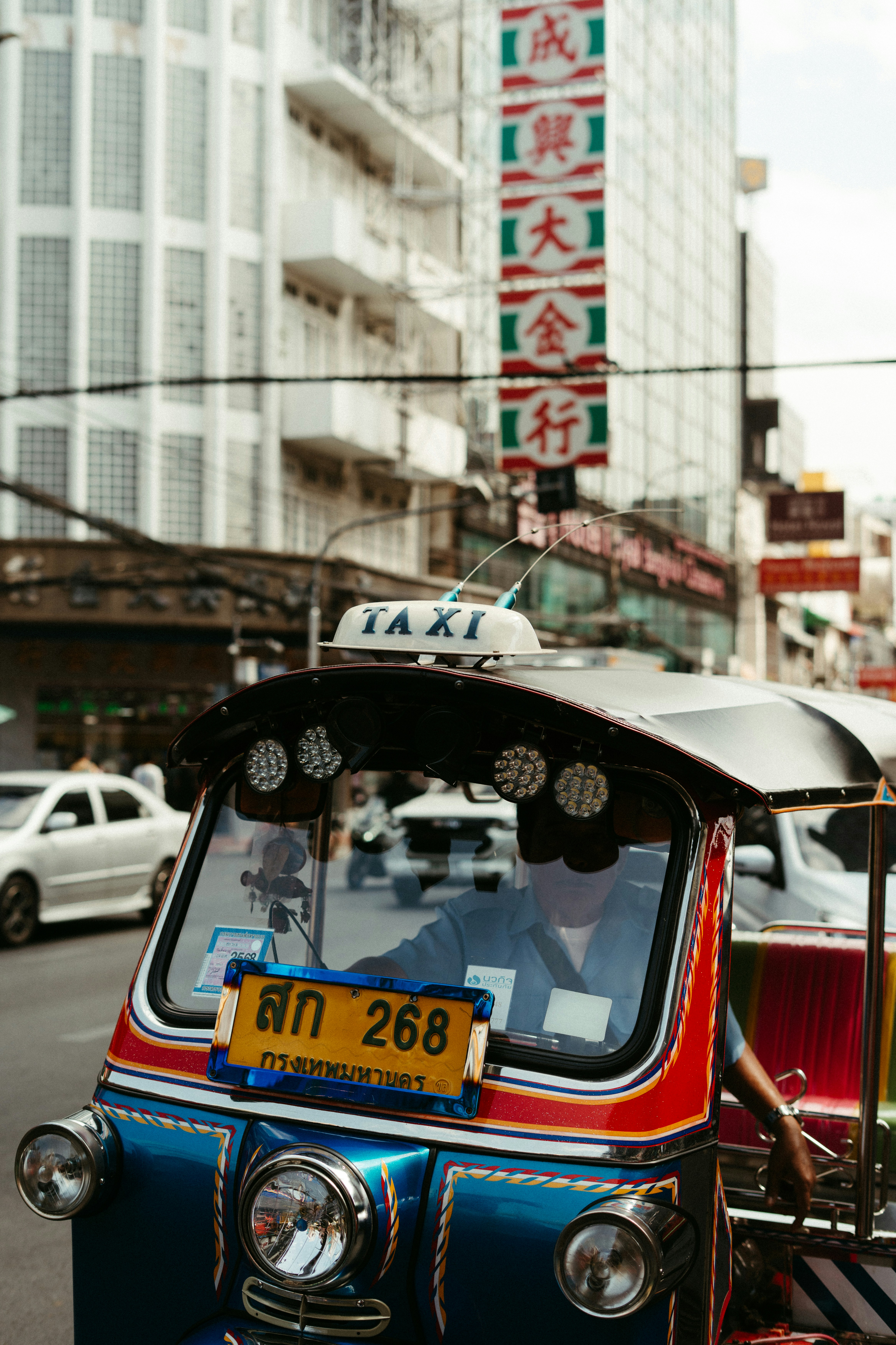 A tuk-tuk taxi is driving on a city street.