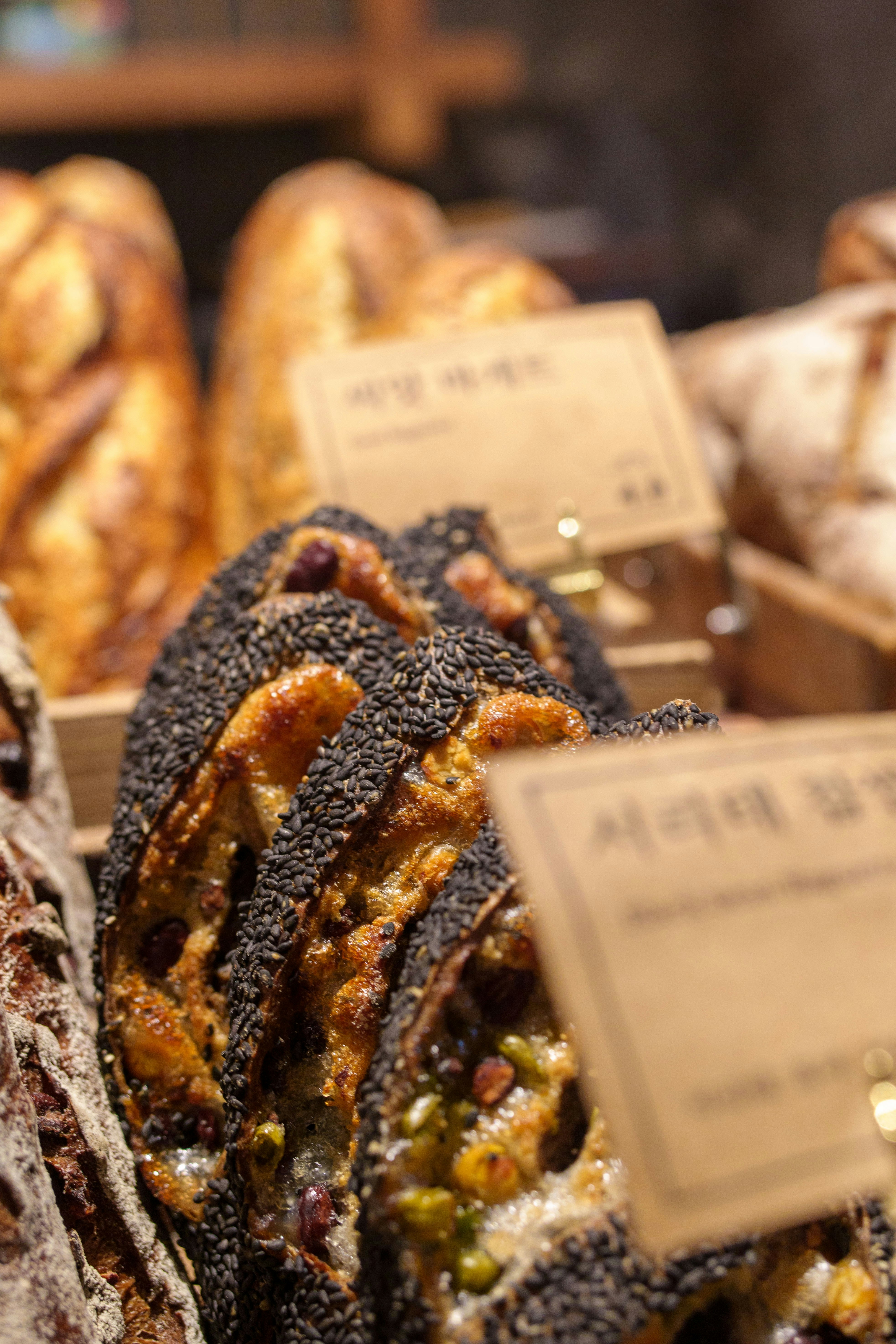 Close-up of assorted donuts with sesame crust and fruit fillings at a bakery counter; blurred background shelves and signage indicate a busy shop. This is a photographic capture of a bakery display.