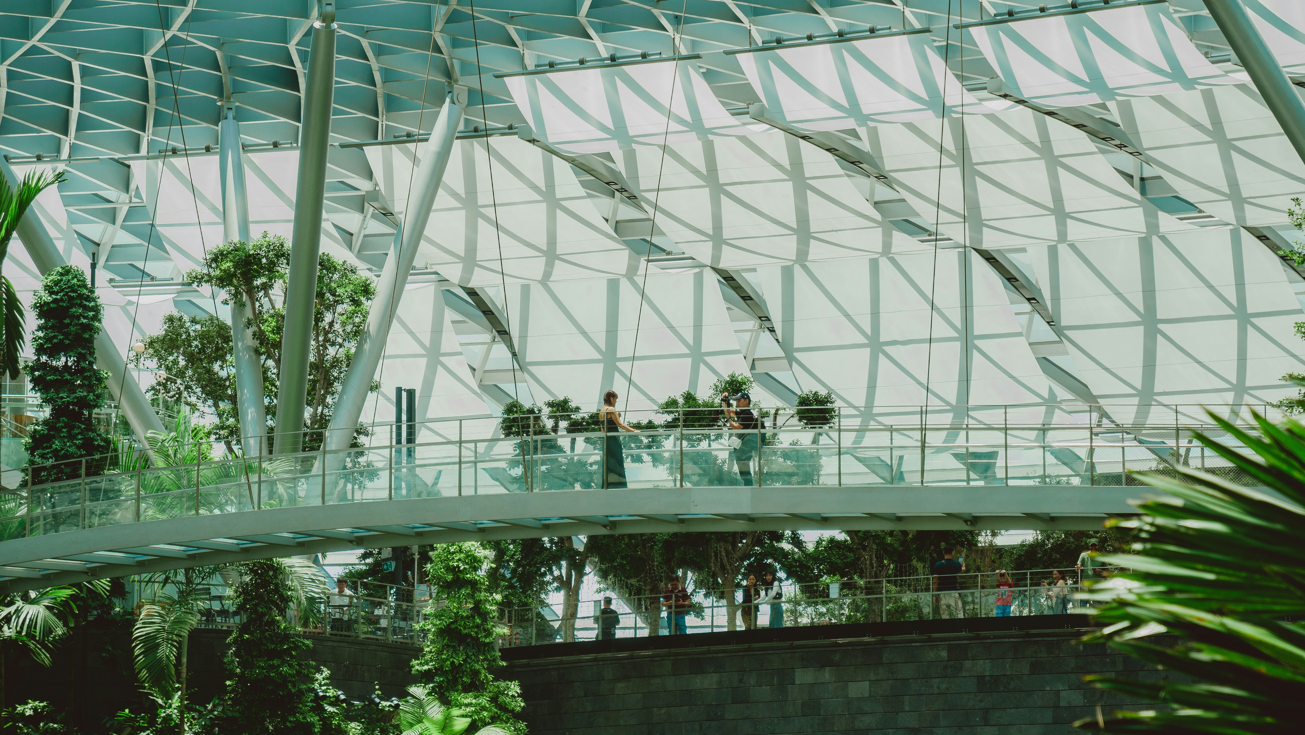 People walk on a glass bridge in a green building.