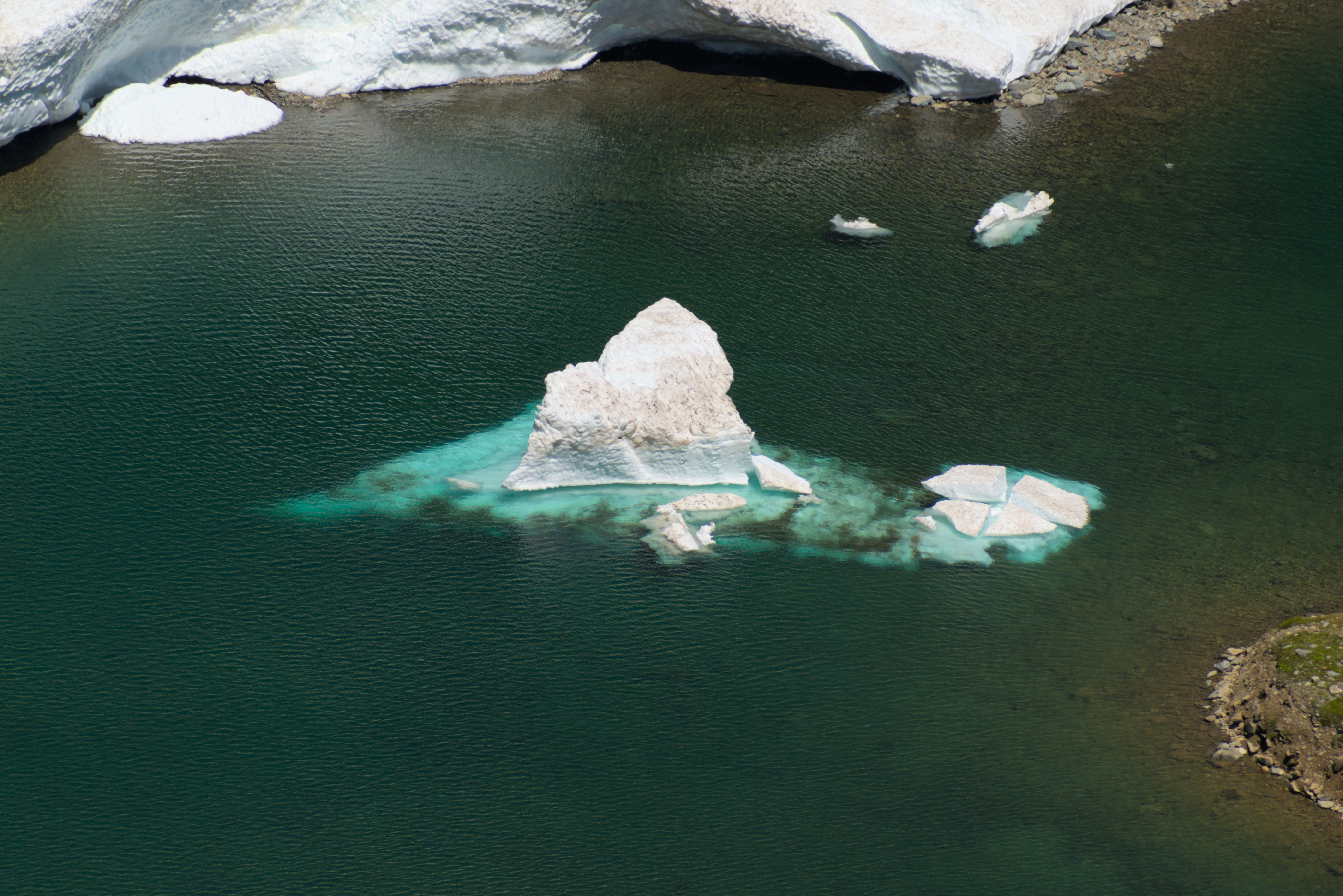 An iceberg floating in a mountain lake. | Icebergs float in a dark, cold body of water.