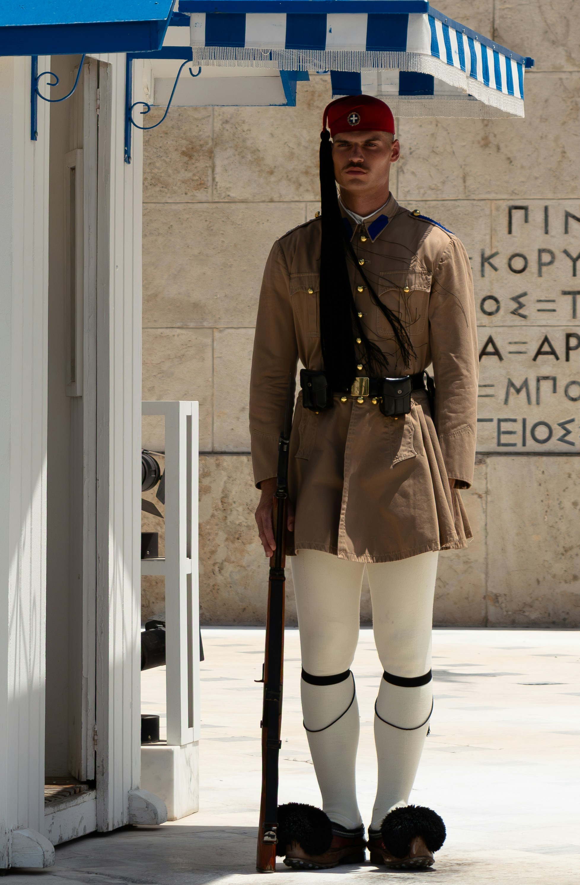 A greek soldier stands guard with a rifle.