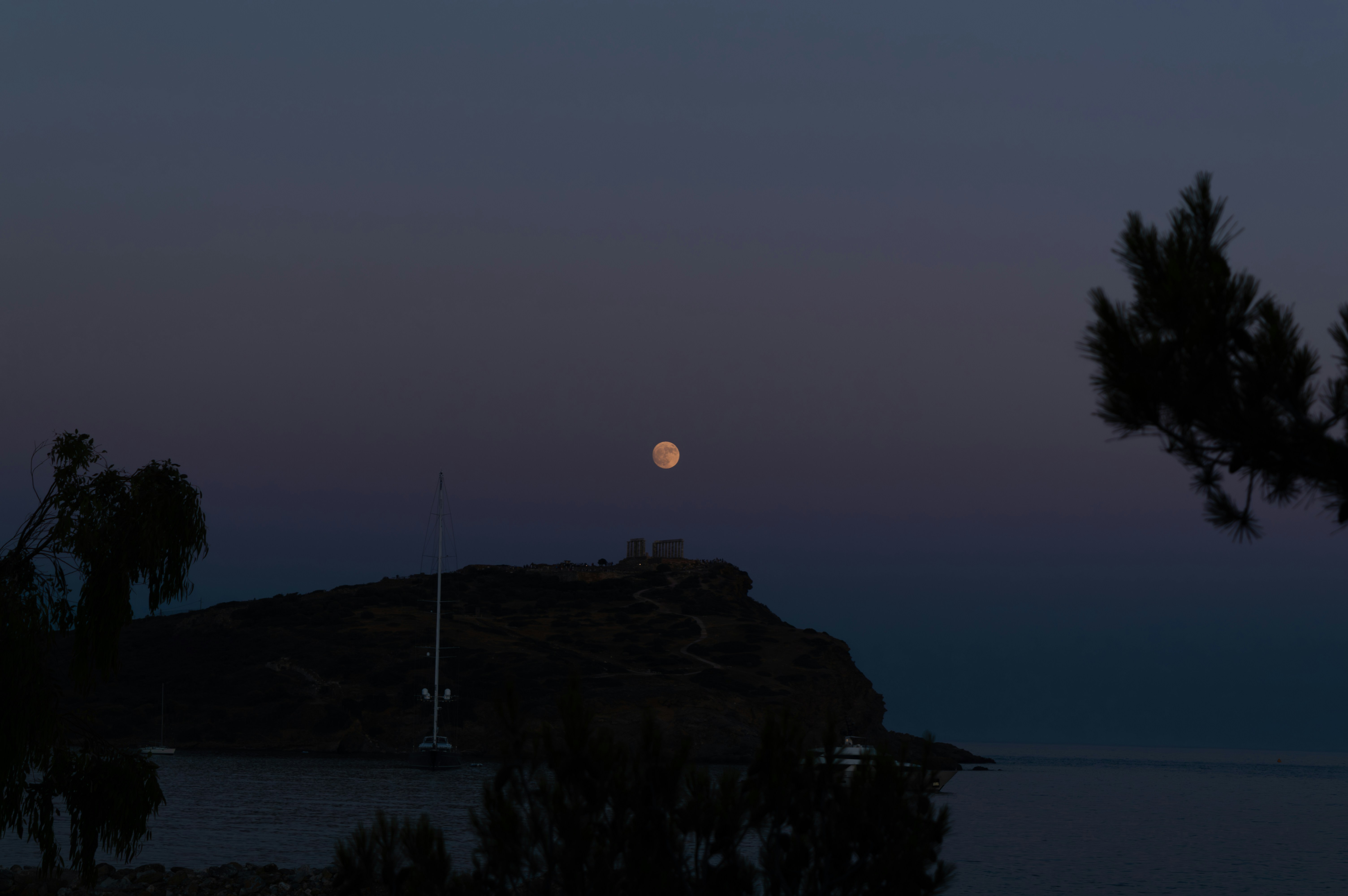 The moon shines over the sea at dusk.