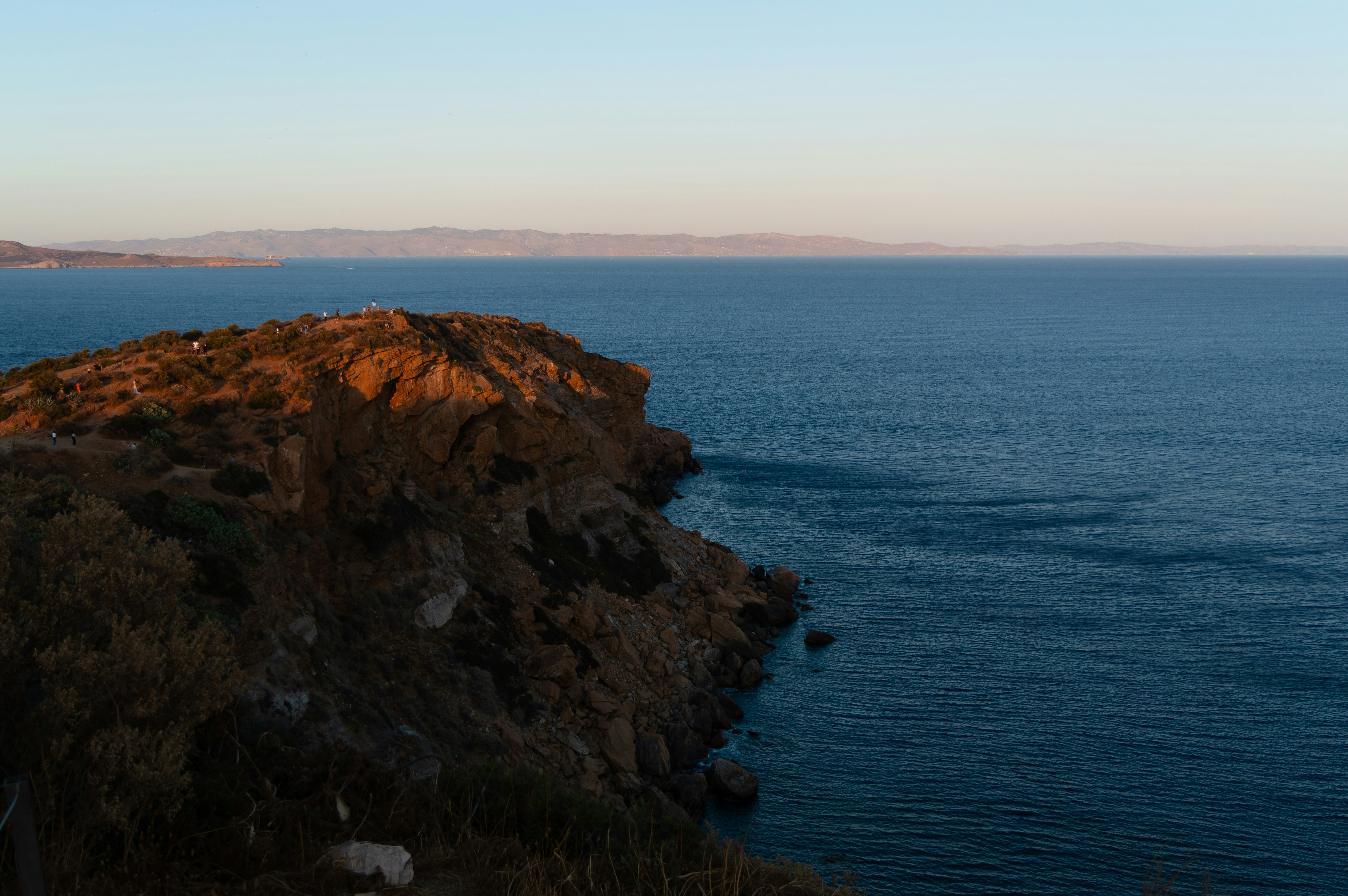 Cliffside overlooks the tranquil sea at sunrise.