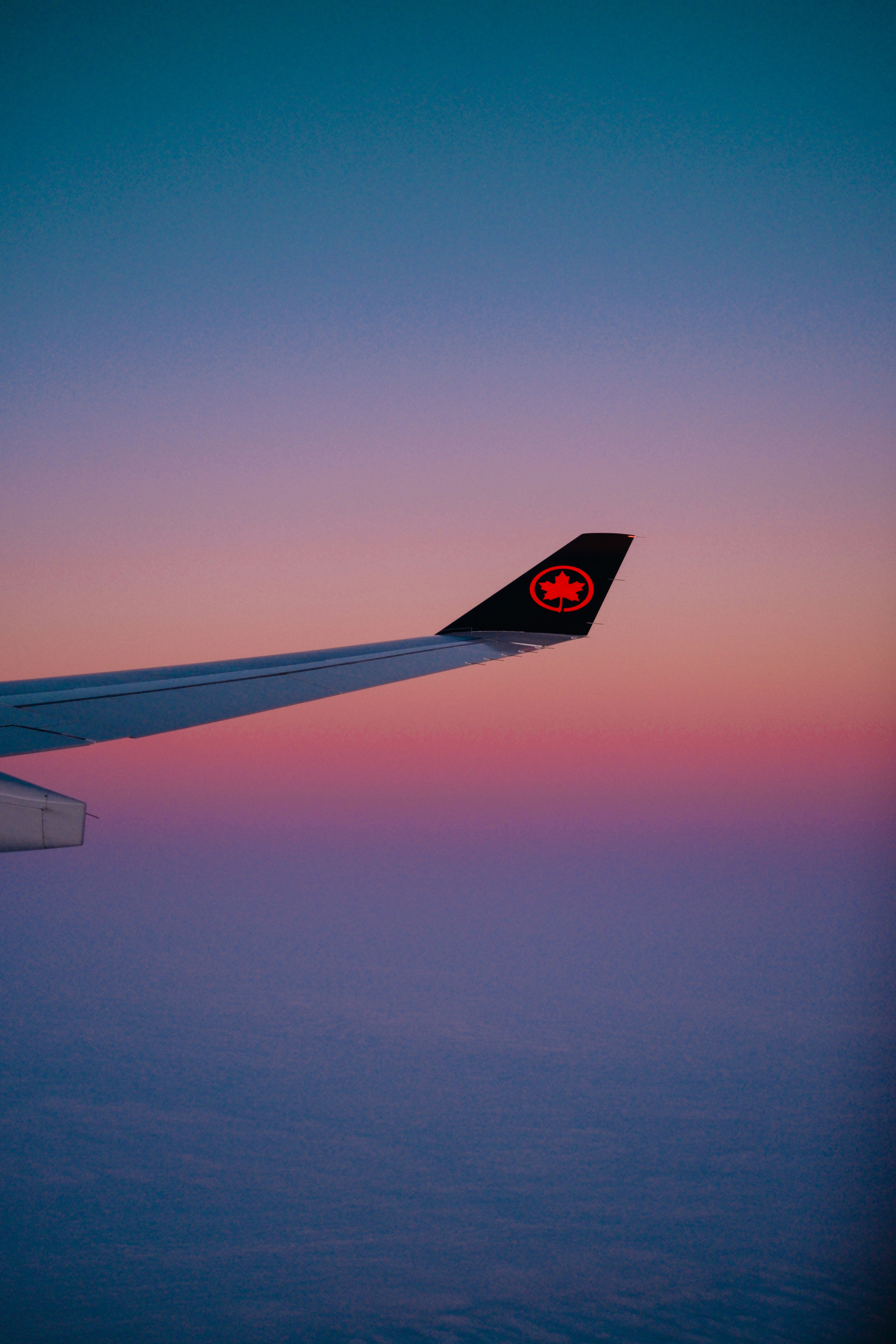 Airplane wing silhouetted against a gradient sky transitioning from deep blue to soft pink at sunset.
