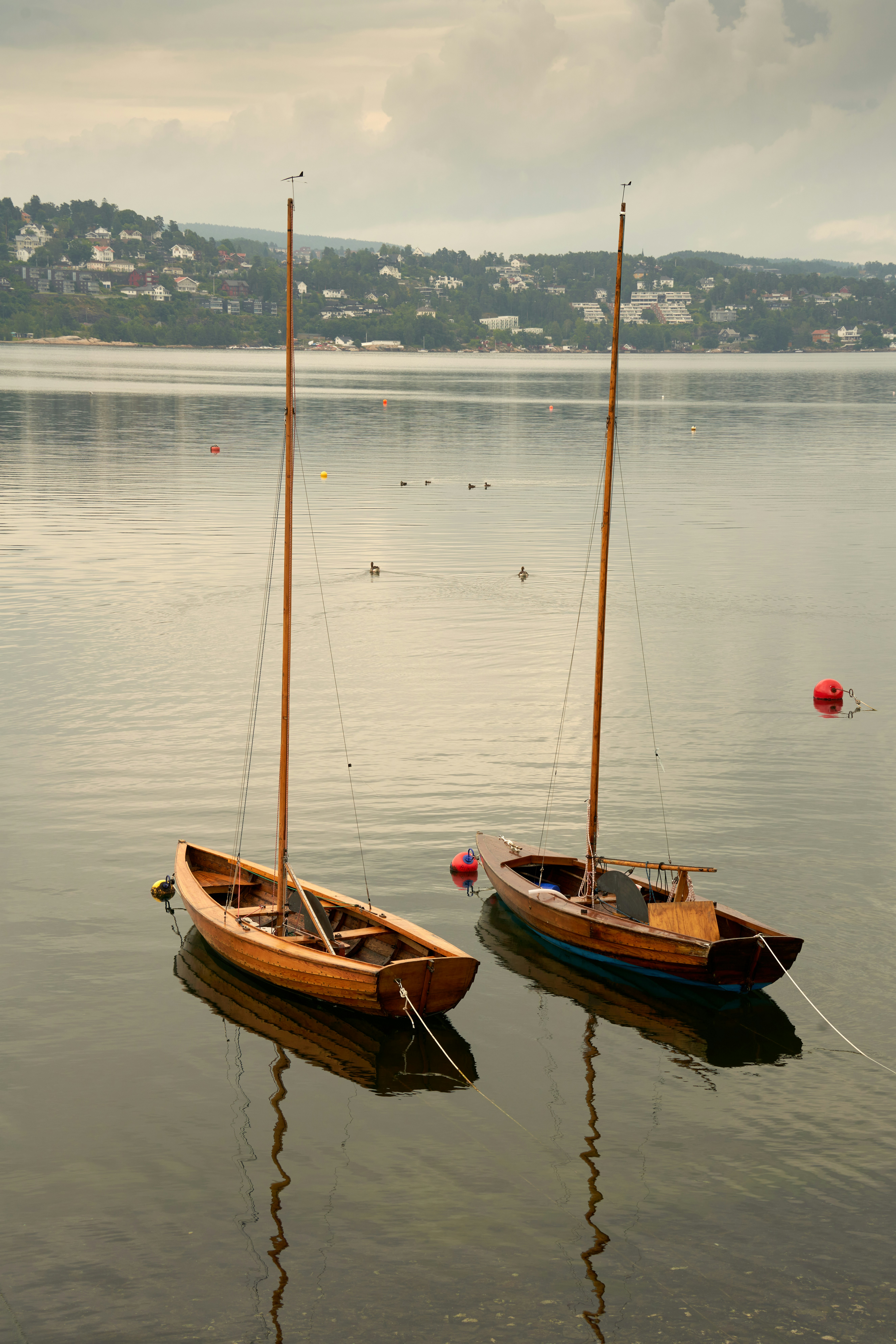 Two small viking style wooden sailing boats are anchored in the Oslo fjord by Ulvøya, Norway | Two small boats float peacefully on the water.