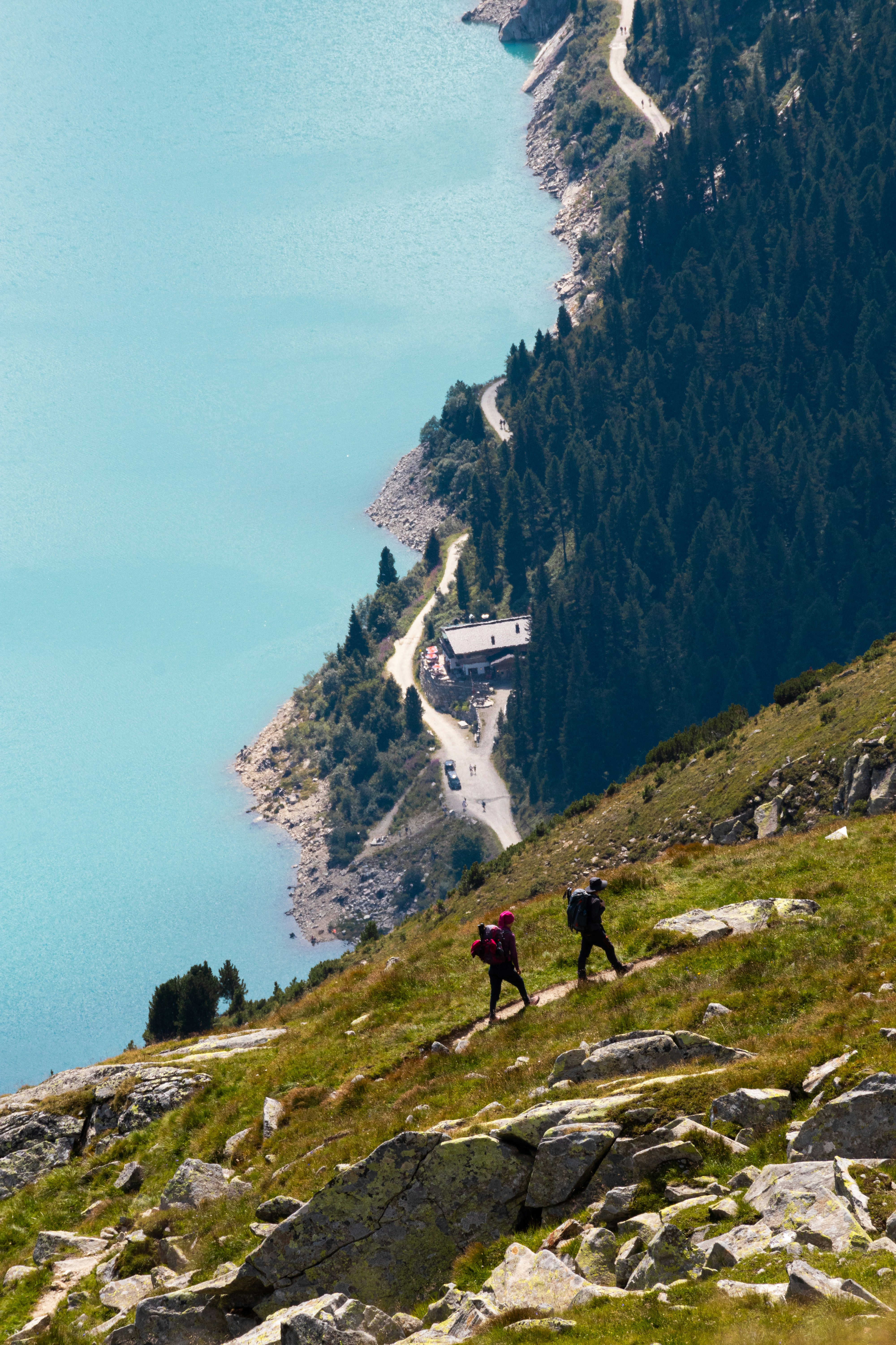 Hikers traverse a mountain, overlooking a lake.