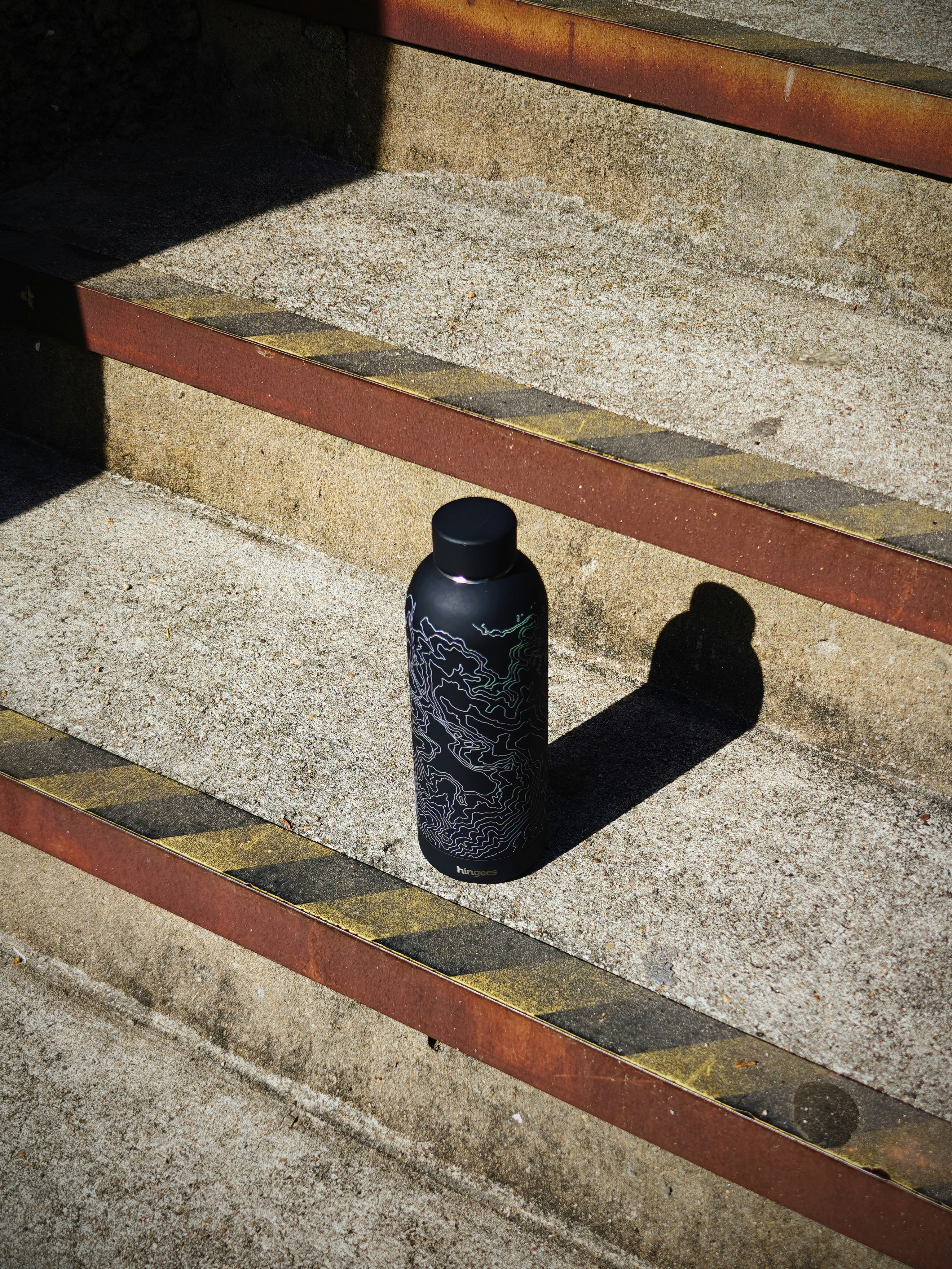 A black bottle rests on concrete steps.