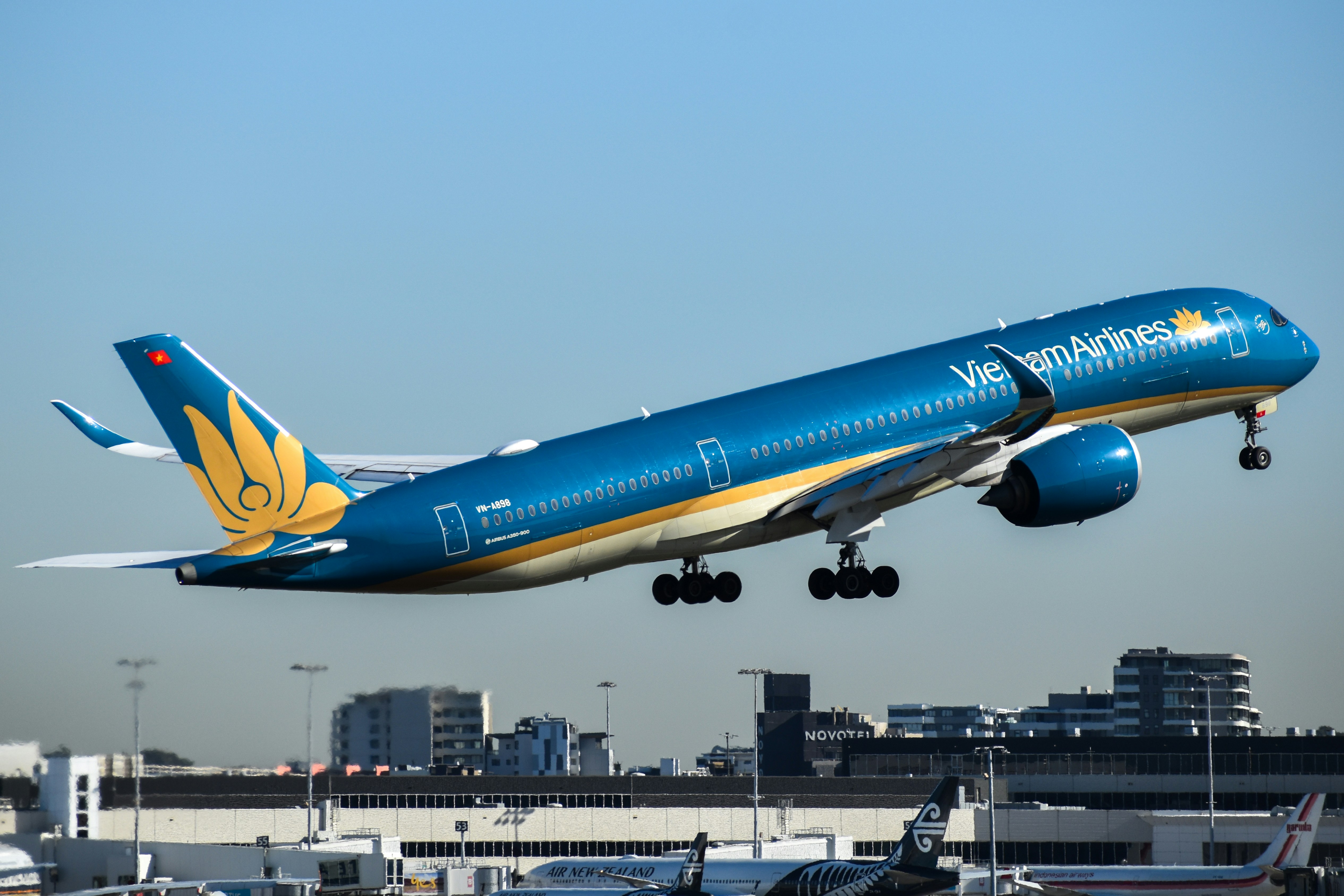 Vietnam Airlines aircraft takes off with a dynamic ascent against an urban backdrop, showcasing modern aviation technology.