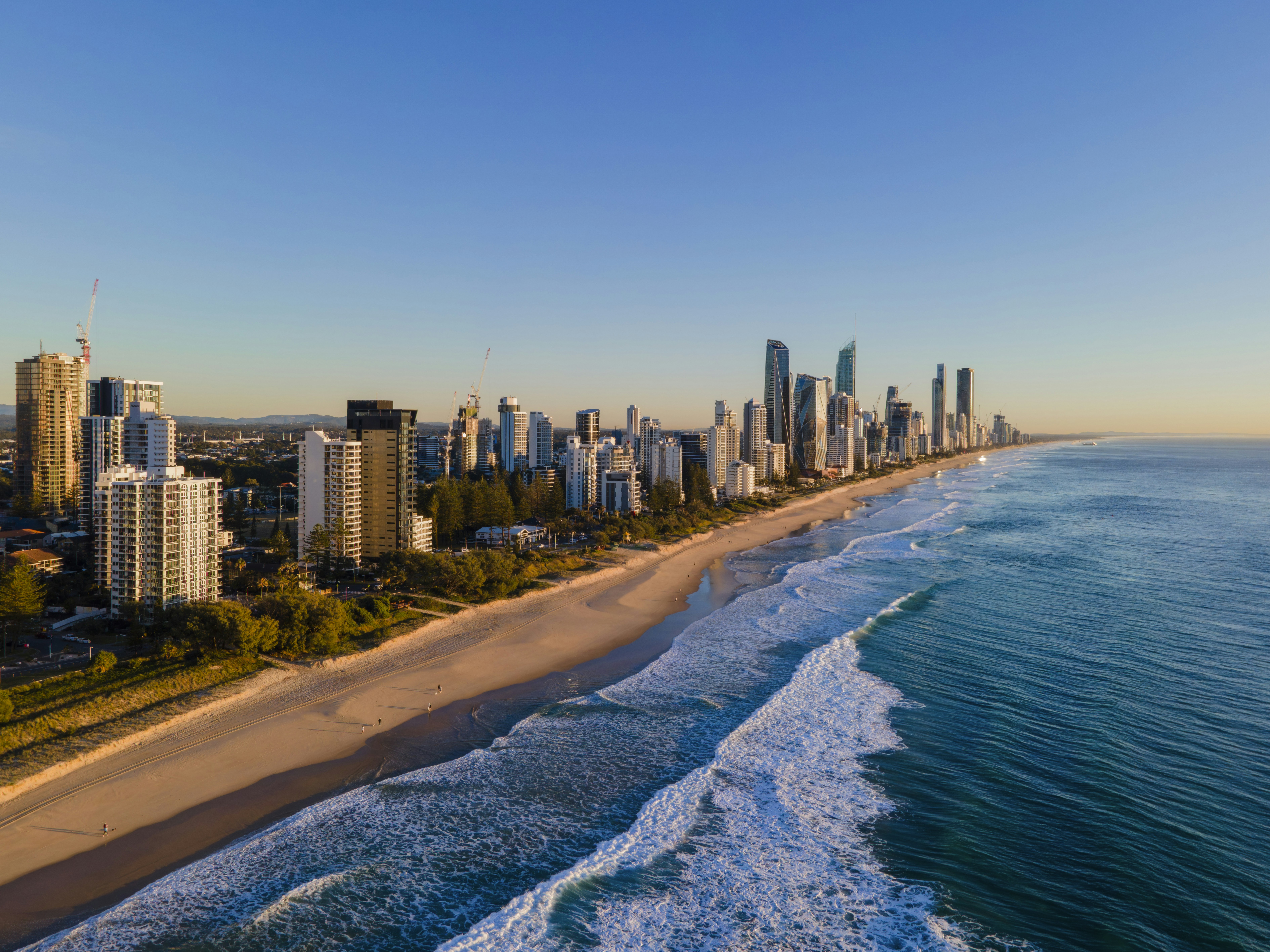 Aerial view of a vibrant coastline with golden sands, high-rise buildings, and gentle waves lapping at the shore.