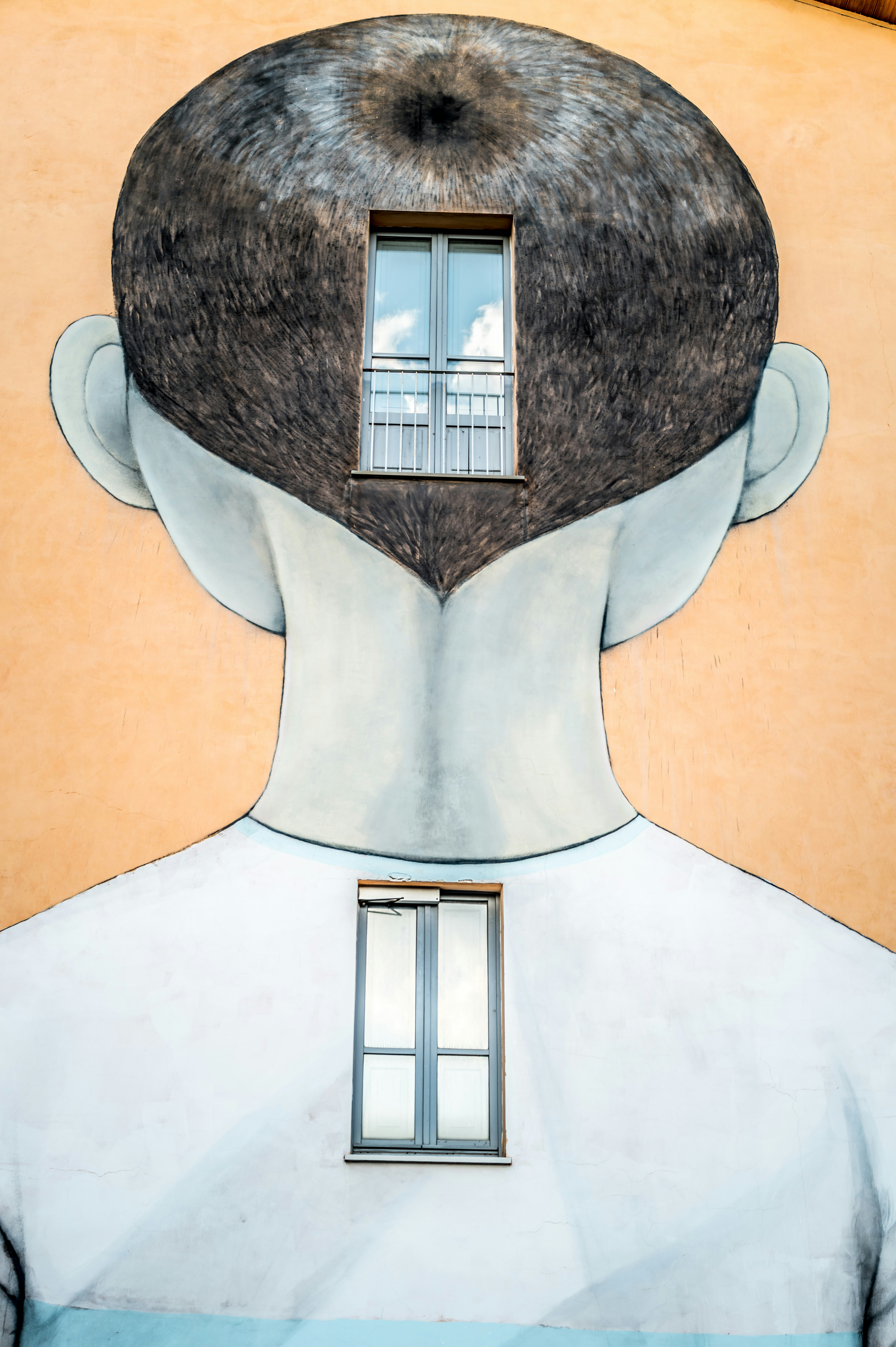 Mural depicting a stylized figure with a window integrated into the hair, set against a warm-toned wall. The artwork challenges perceptions of space and perspective.